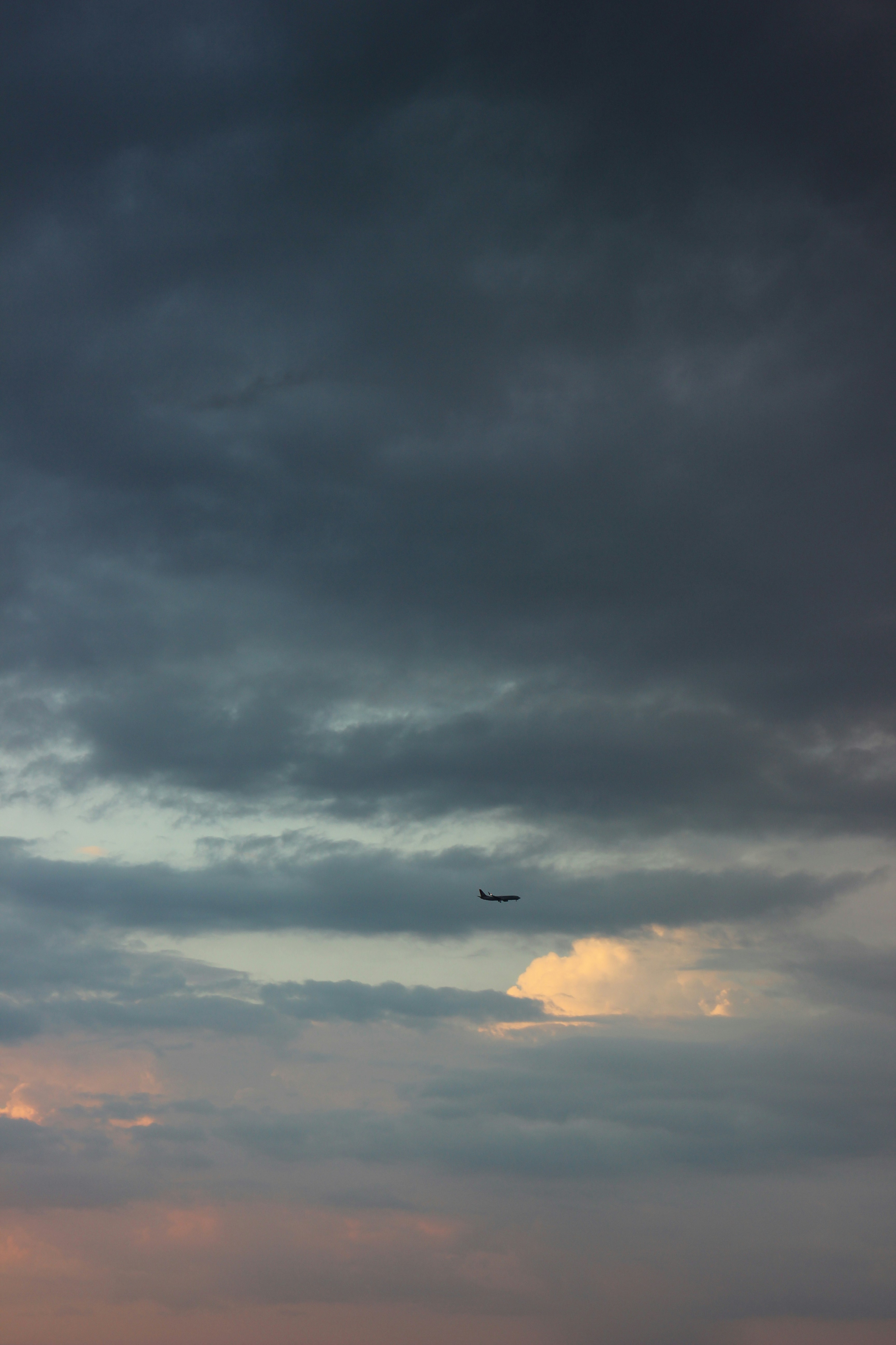 An airplane glides through a dramatic sky filled with swirling clouds and hints of sunset colors.