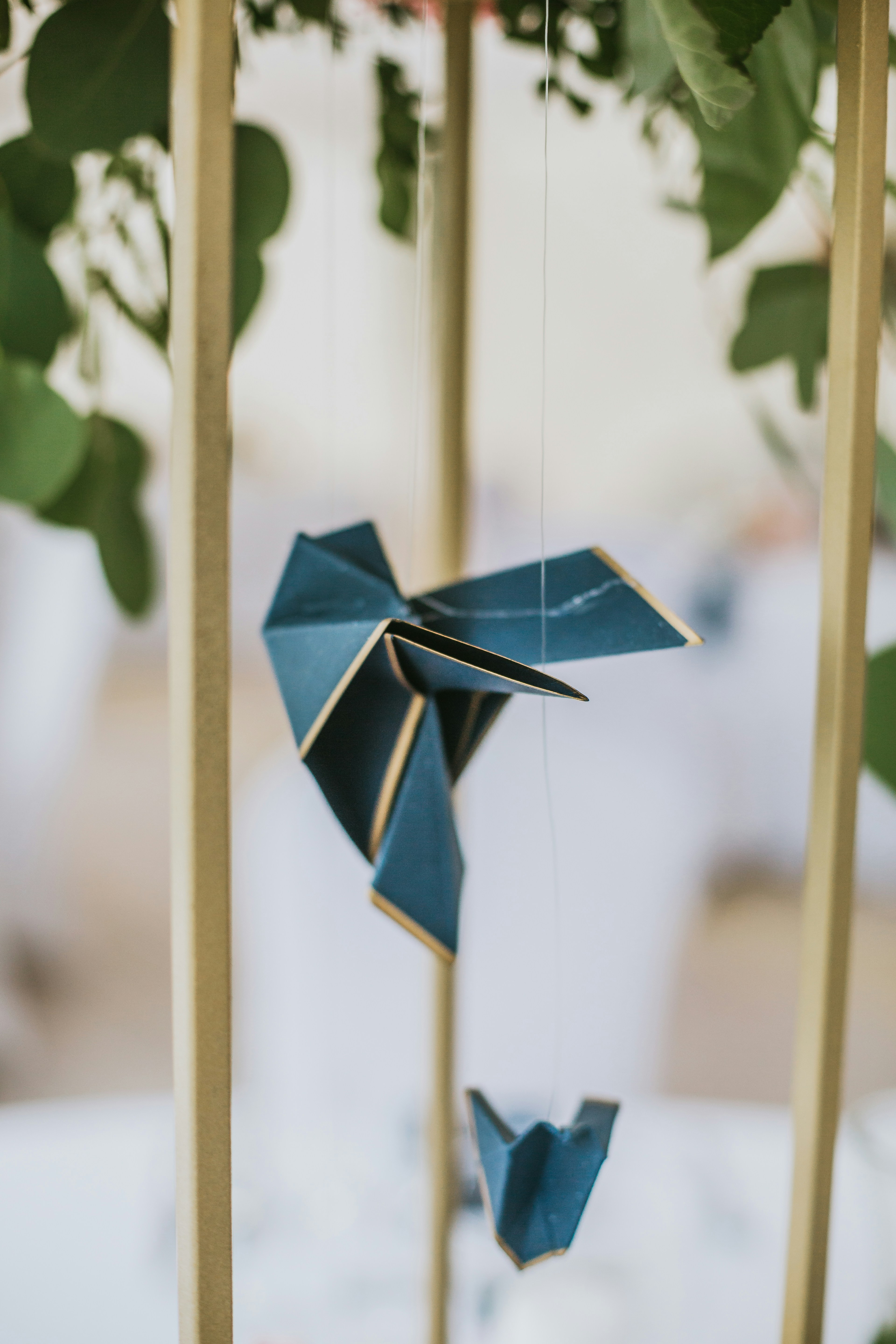 Intricately folded blue origami shapes suspended amidst greenery, showcasing a blend of craftsmanship and nature's beauty.