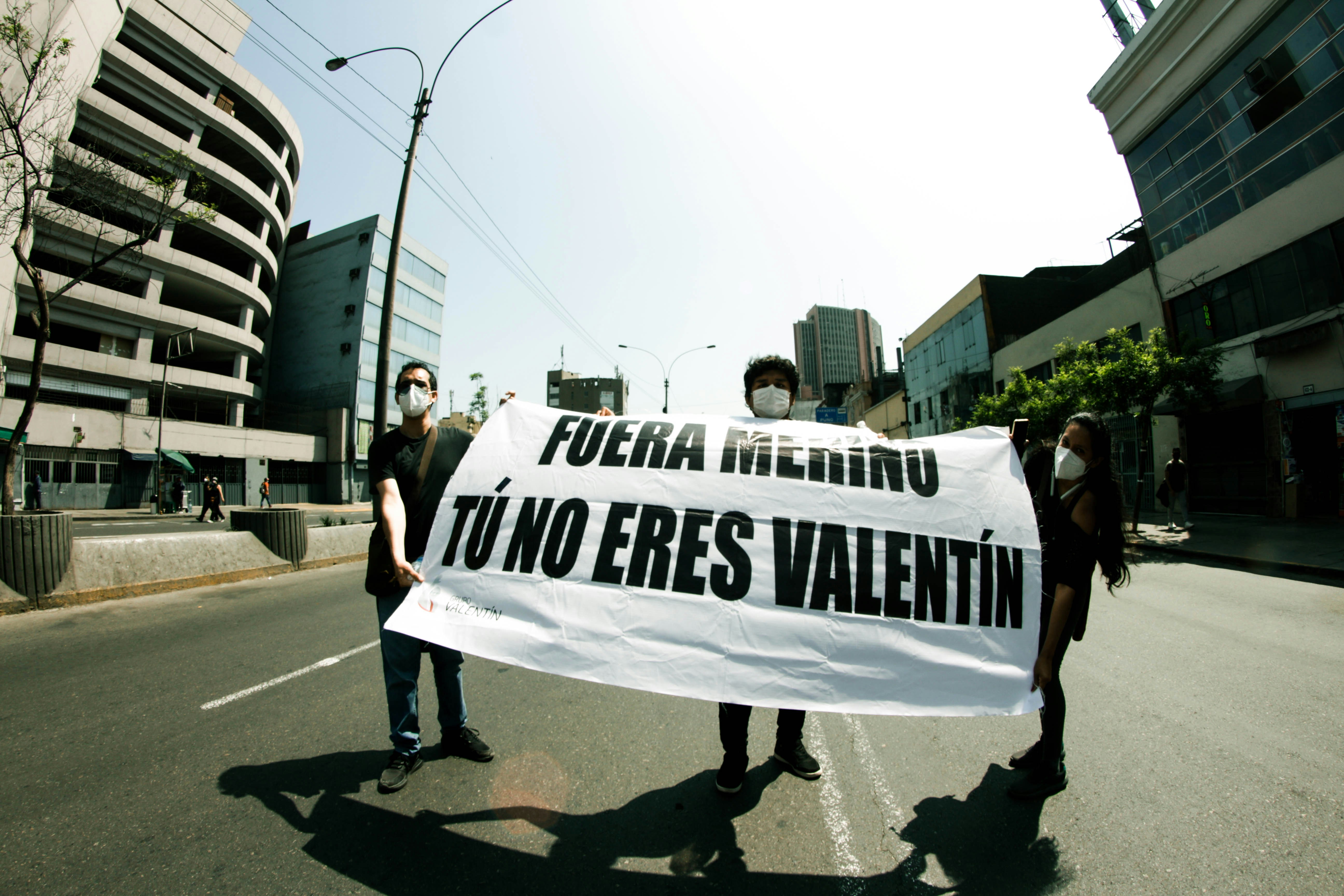 Activists holding a large banner reading 'Fuera Melino, Tú no eres Valentín' during a protest on a city street.