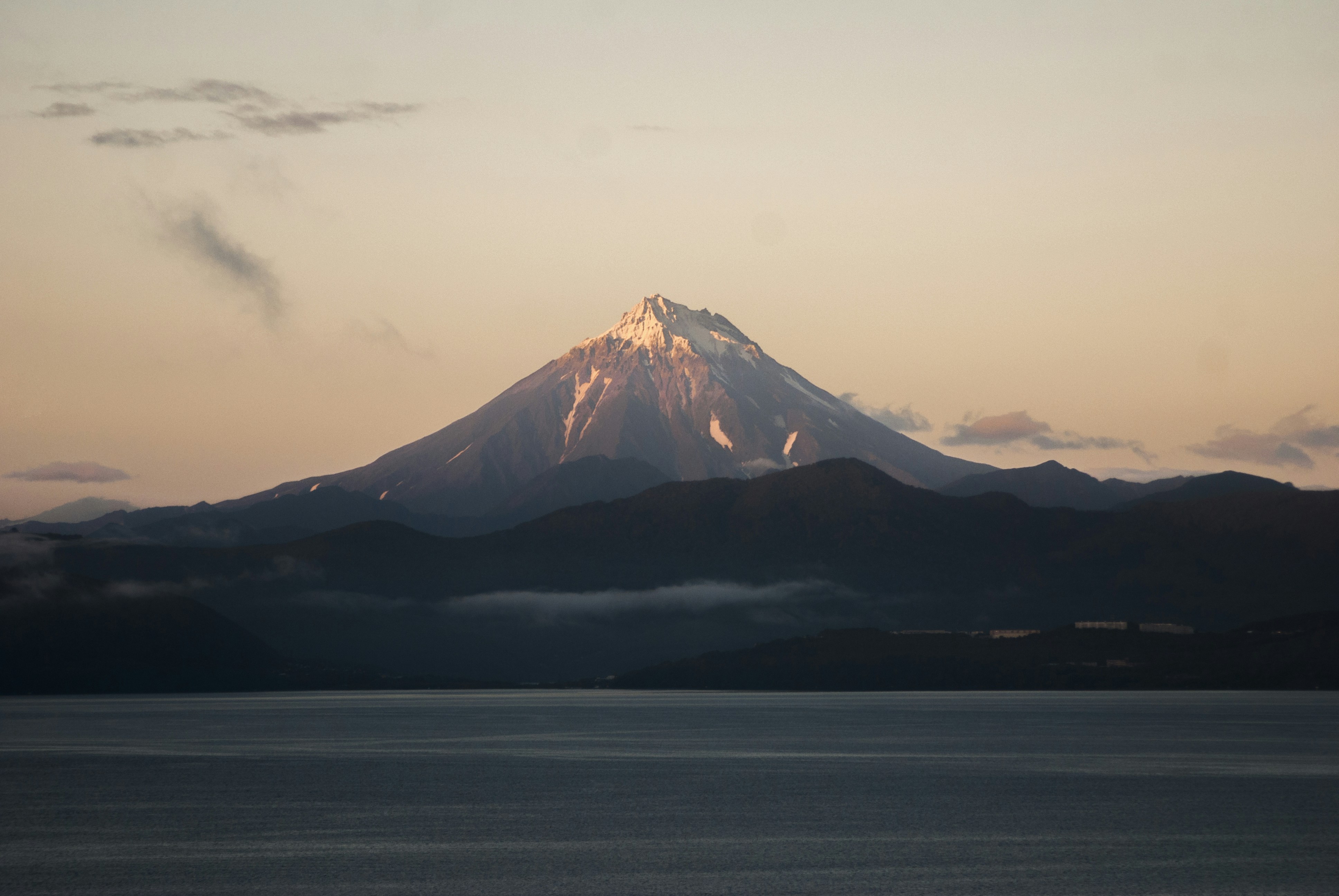 Snow-capped volcano rises majestically against a pastel sky, reflecting the serene waters below.