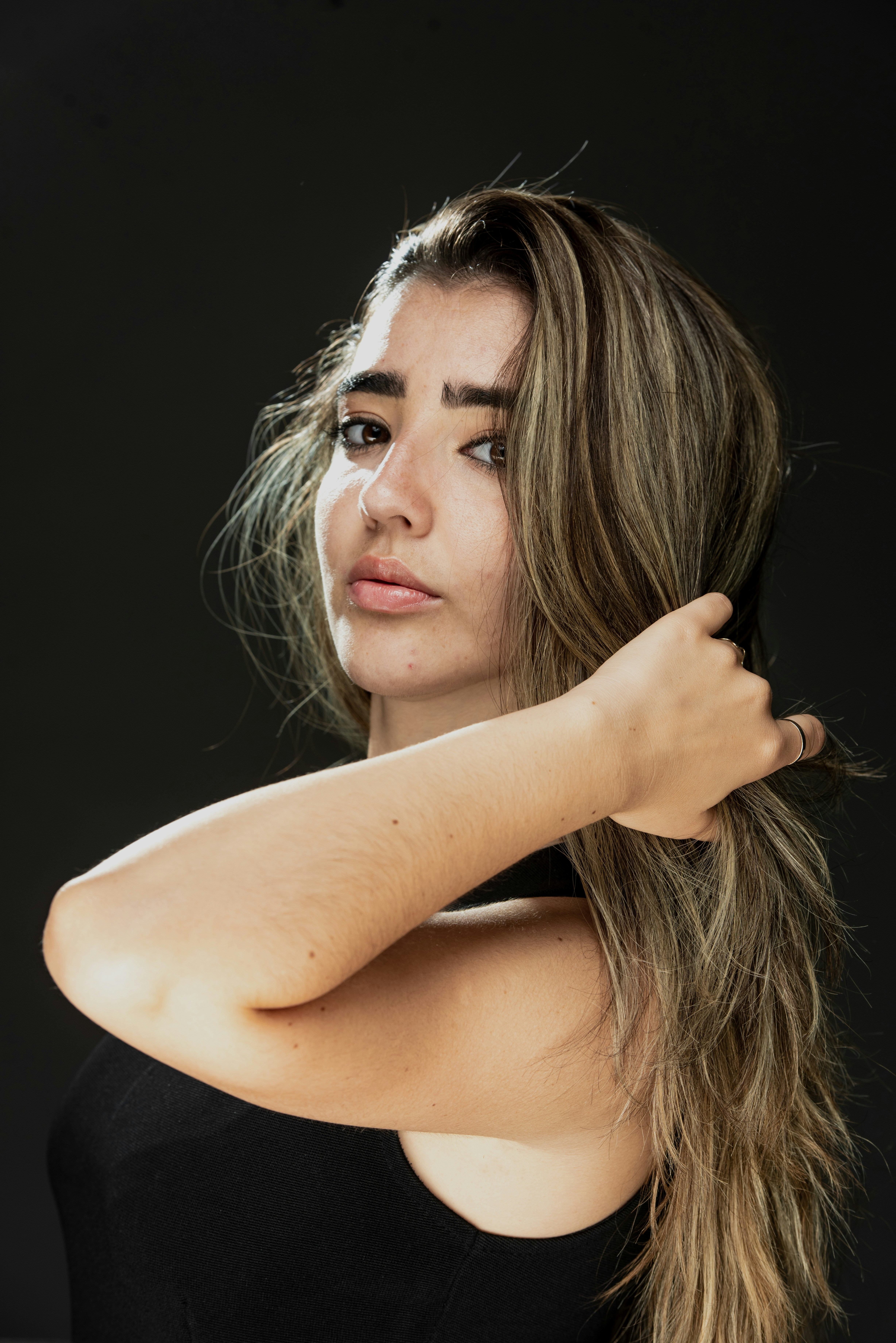 Model gracefully adjusting her hair against a dark backdrop, showcasing a blend of confidence and serenity.