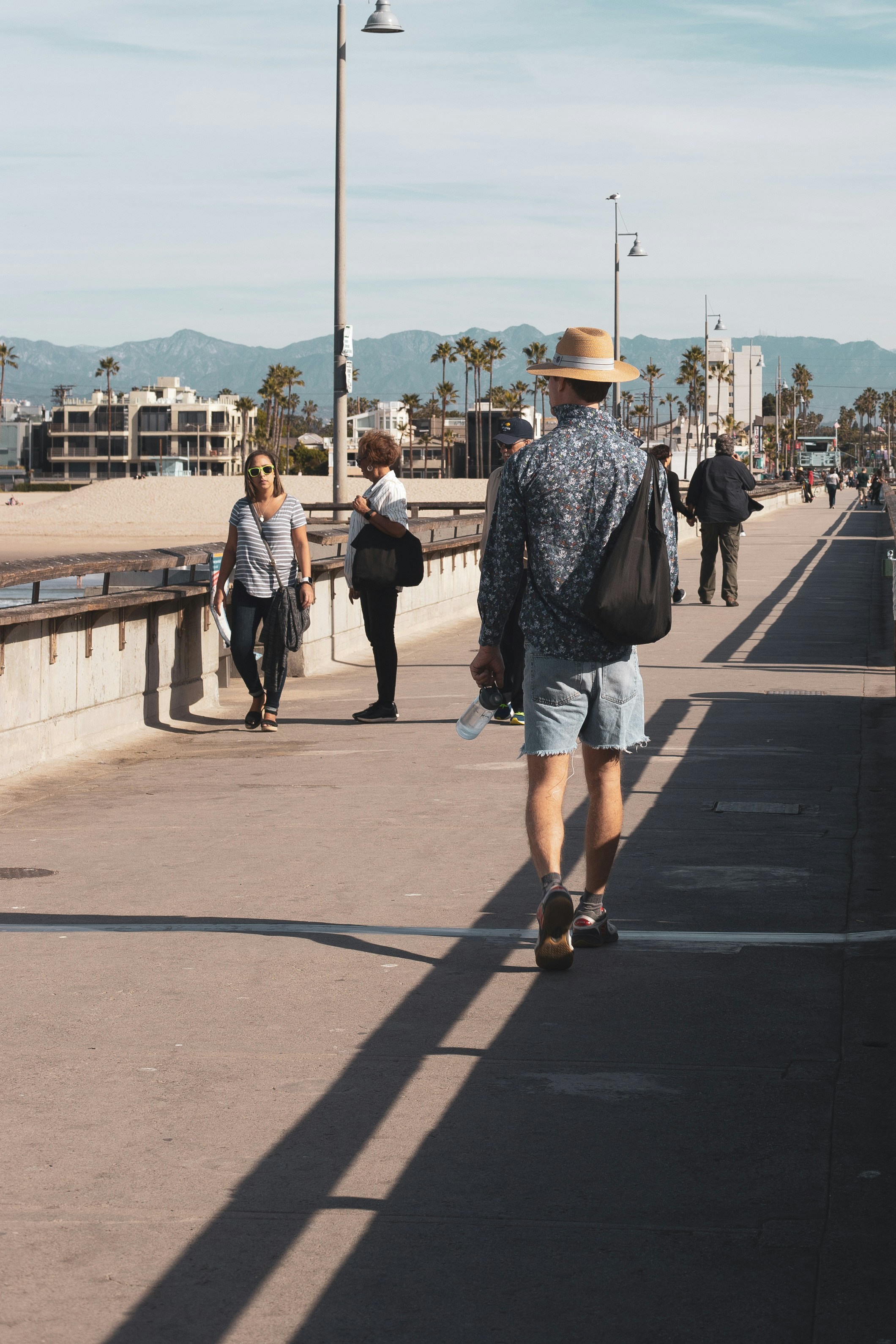 Sunlit Stride: The Hat-Wearing Wanderer on a Seaside Boardwalk