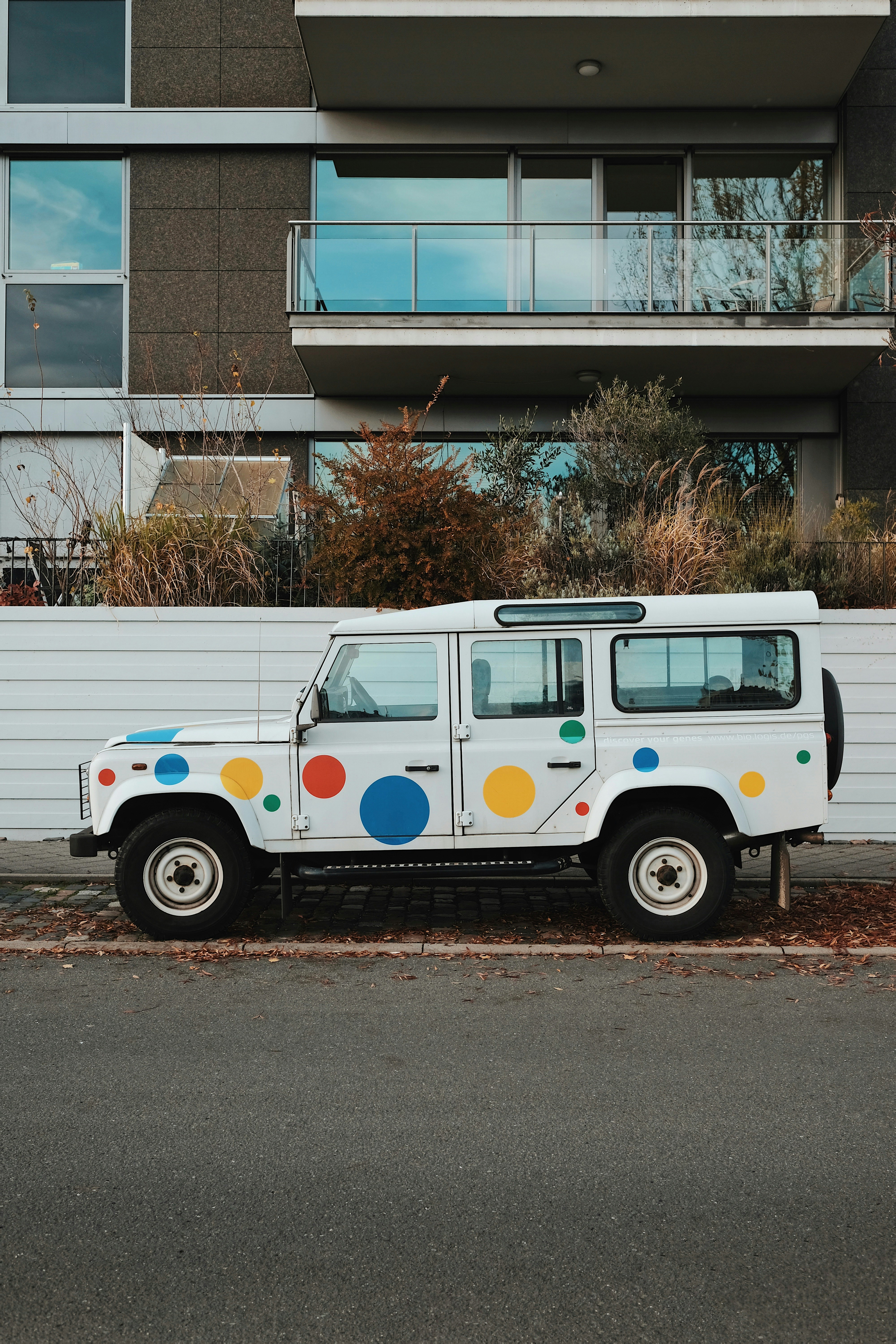 A vintage white vehicle adorned with colorful polka dots parked beside a modern building, showcasing a blend of classic and contemporary design elements.