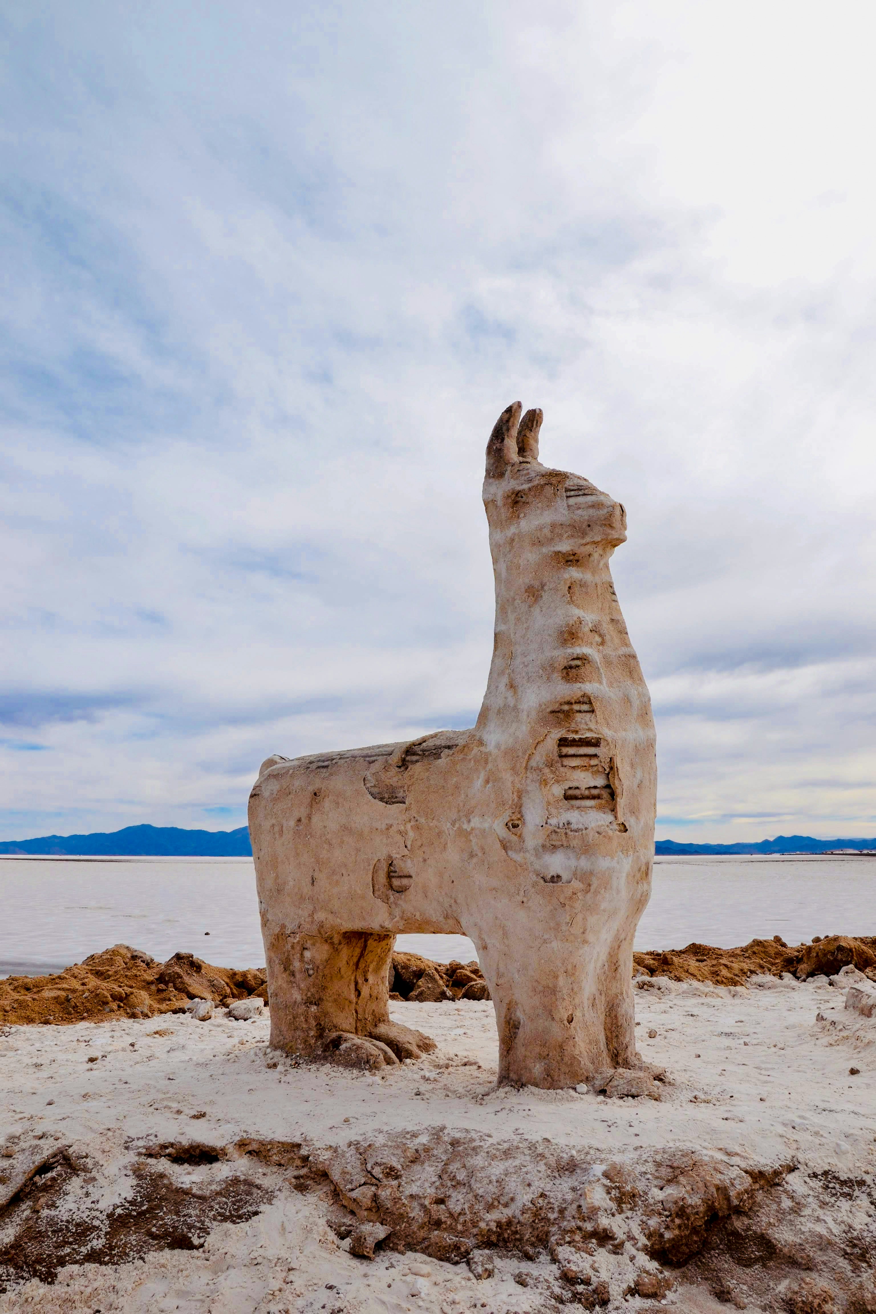 A weathered sculpture resembling a llama stands amidst the salt flats, reflecting the artistry of local culture against a backdrop of expansive skies.