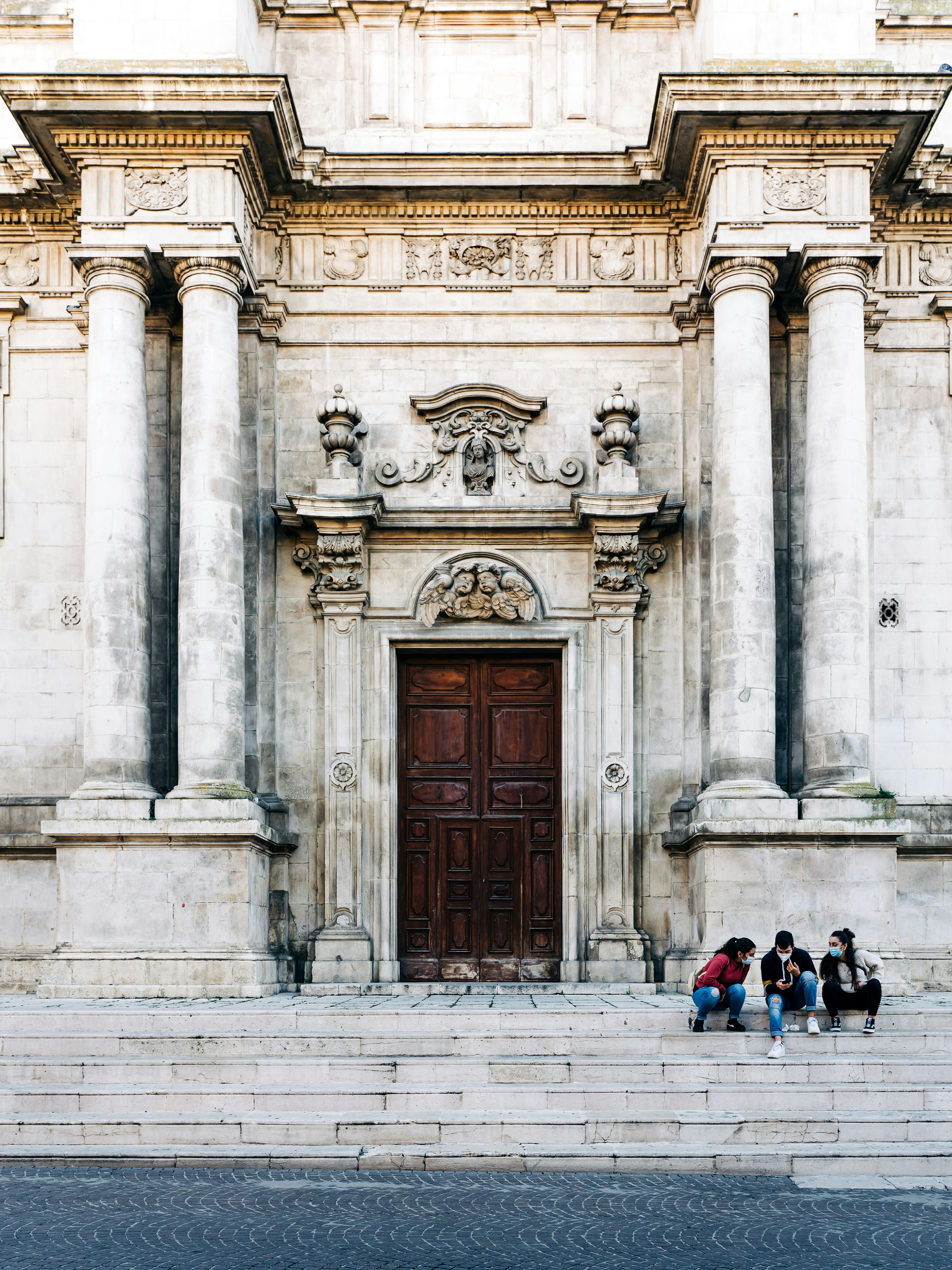 Baroque Portal, Quiet Steps: Four Friends Rest on a Grand Facade