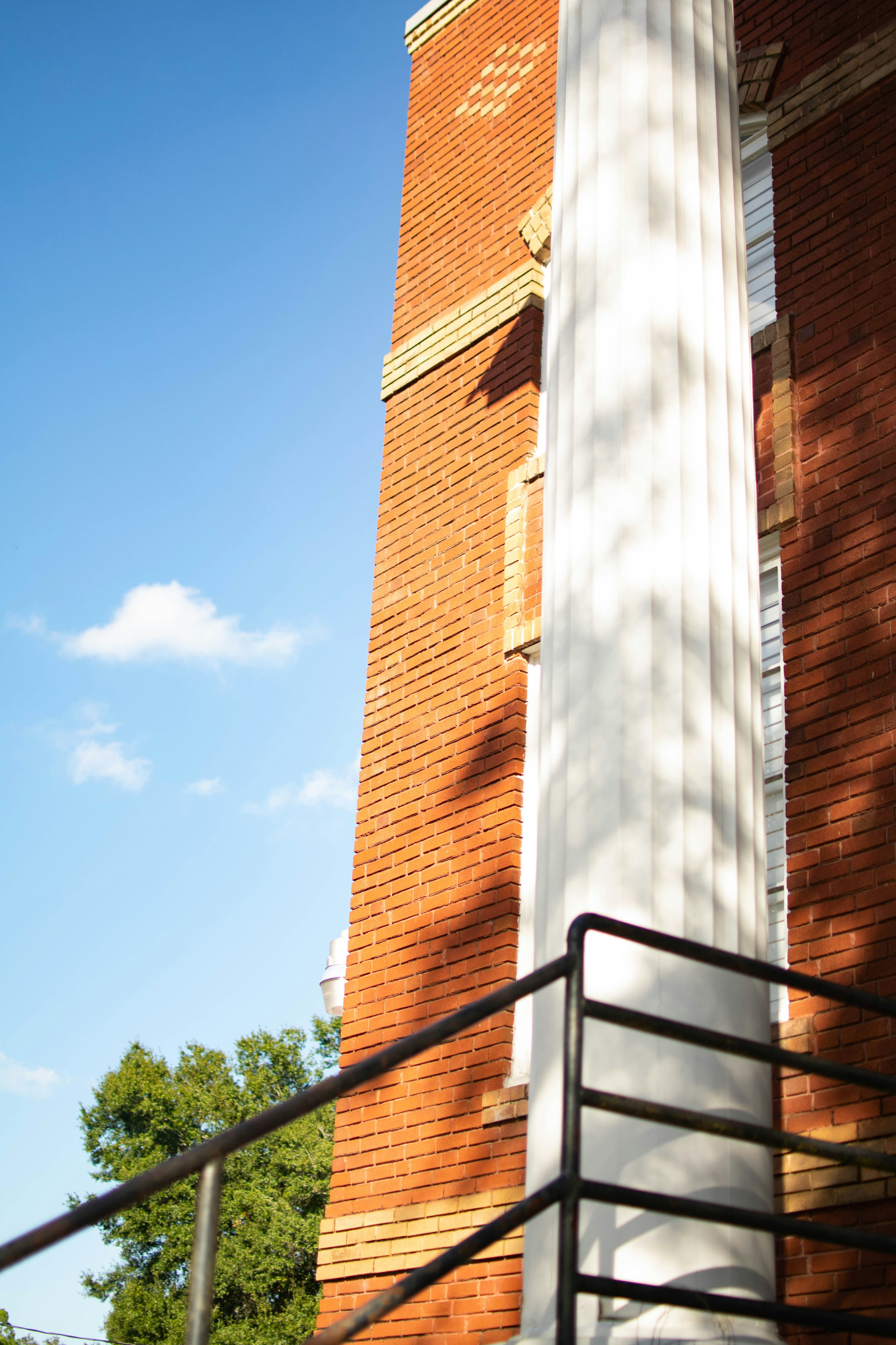 Close-up of a brick building featuring a tall white column and intricate architectural details against a blue sky.