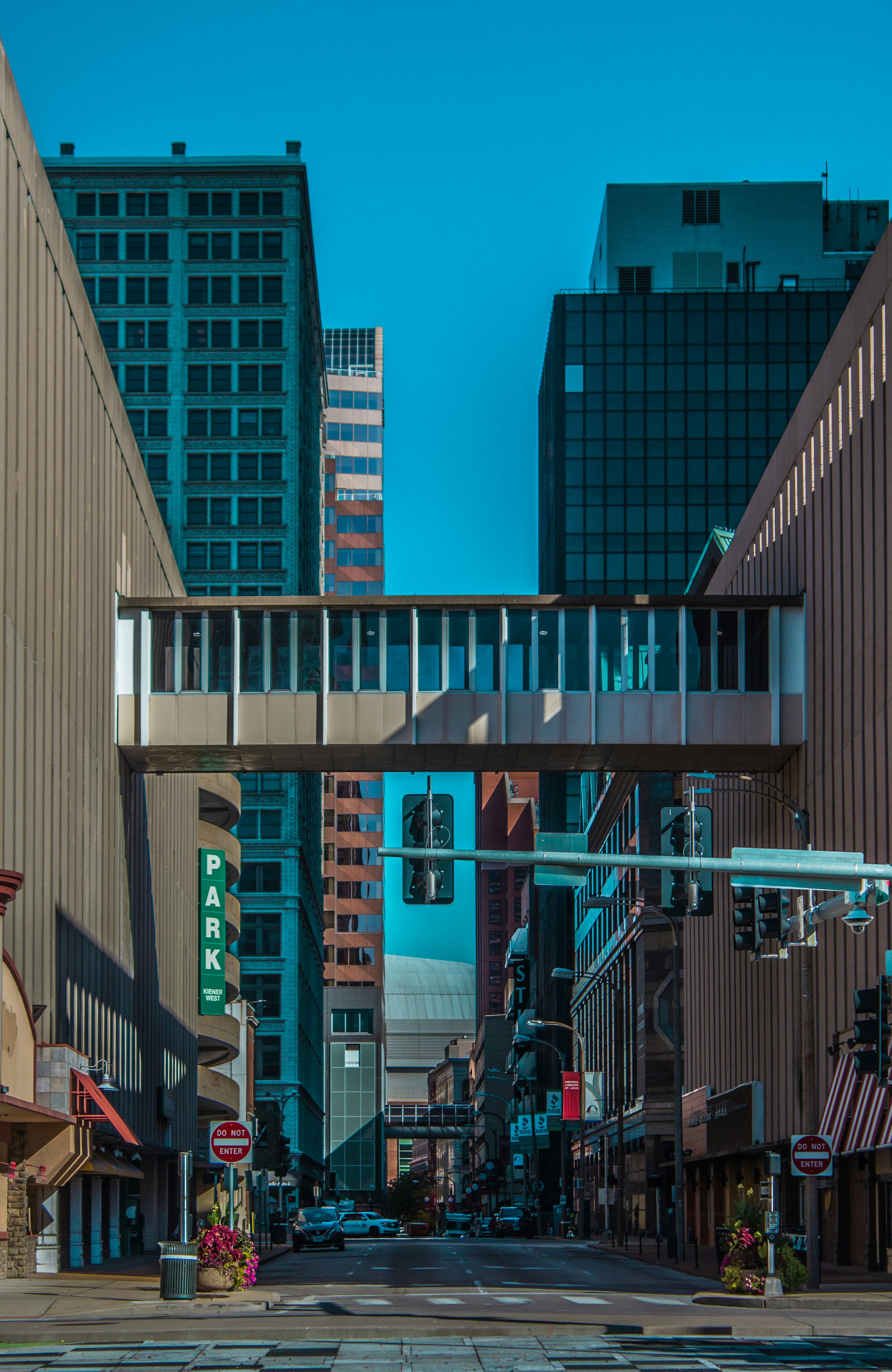 A modern pedestrian overpass connects buildings in a bustling urban environment, framed by towering skyscrapers and vibrant street signage.