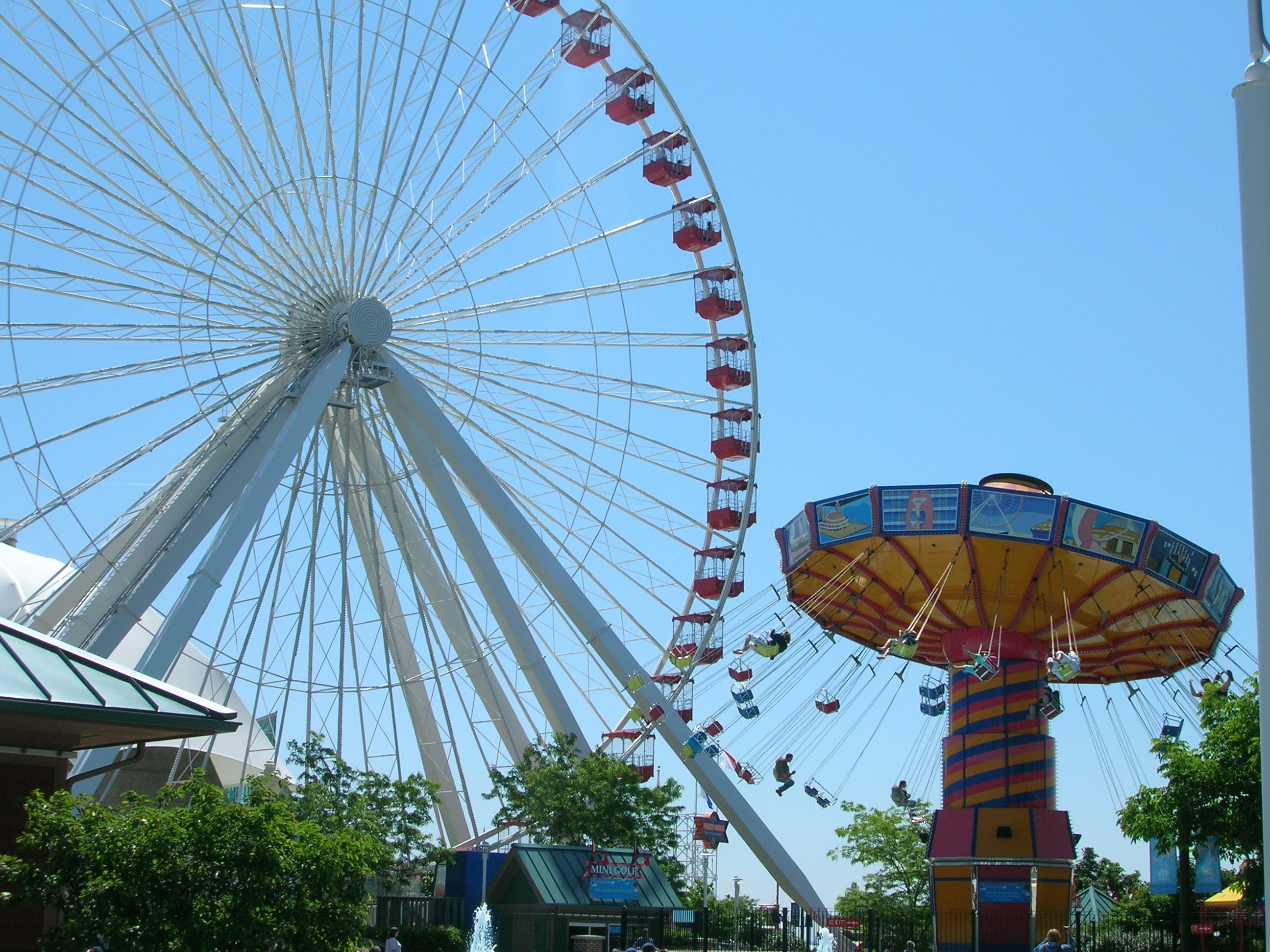 Ferris wheel towering over colorful swing ride in a vibrant amusement park setting under a clear blue sky.