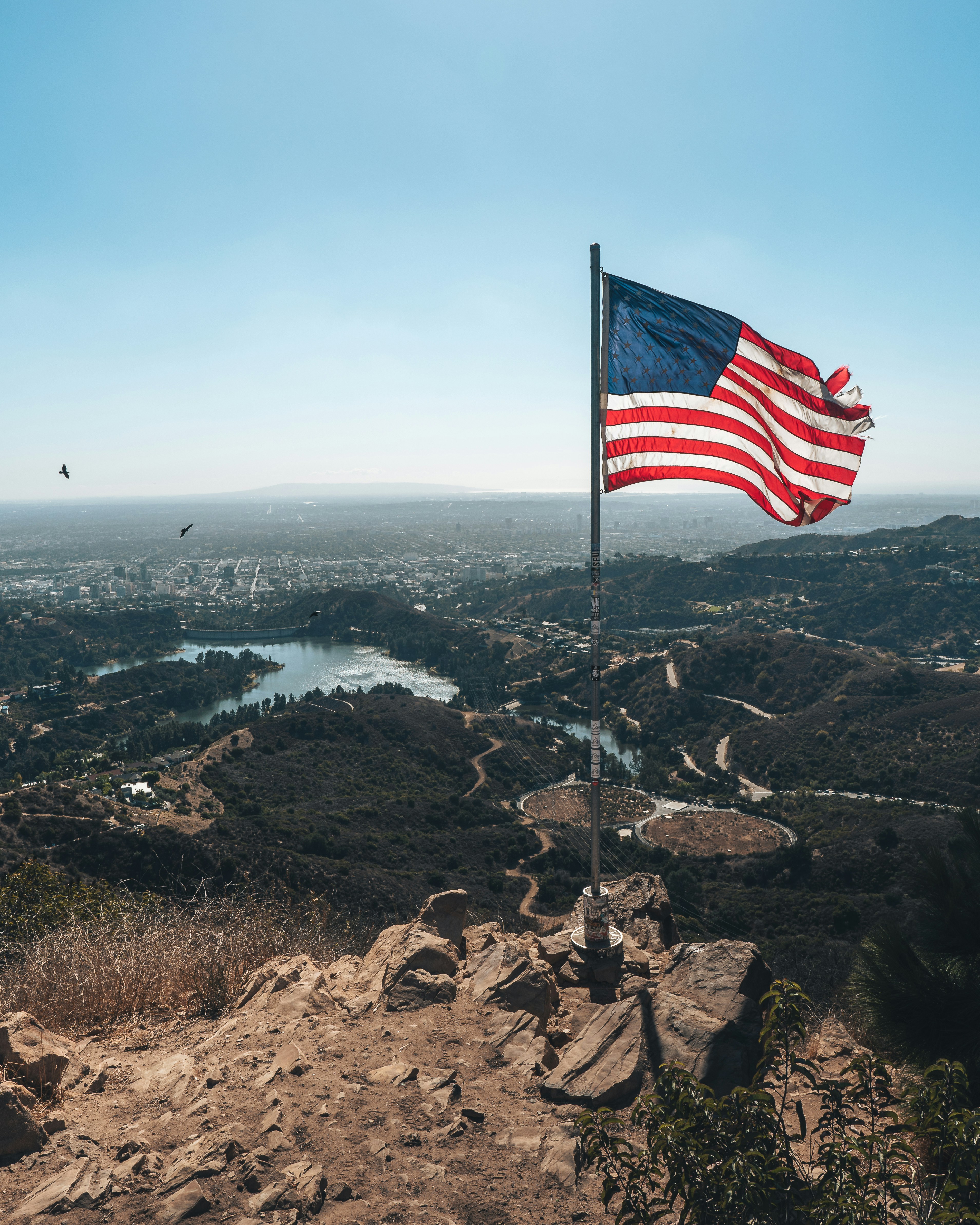American flag billowing in the wind atop a hill, overlooking a serene lake and valley below.