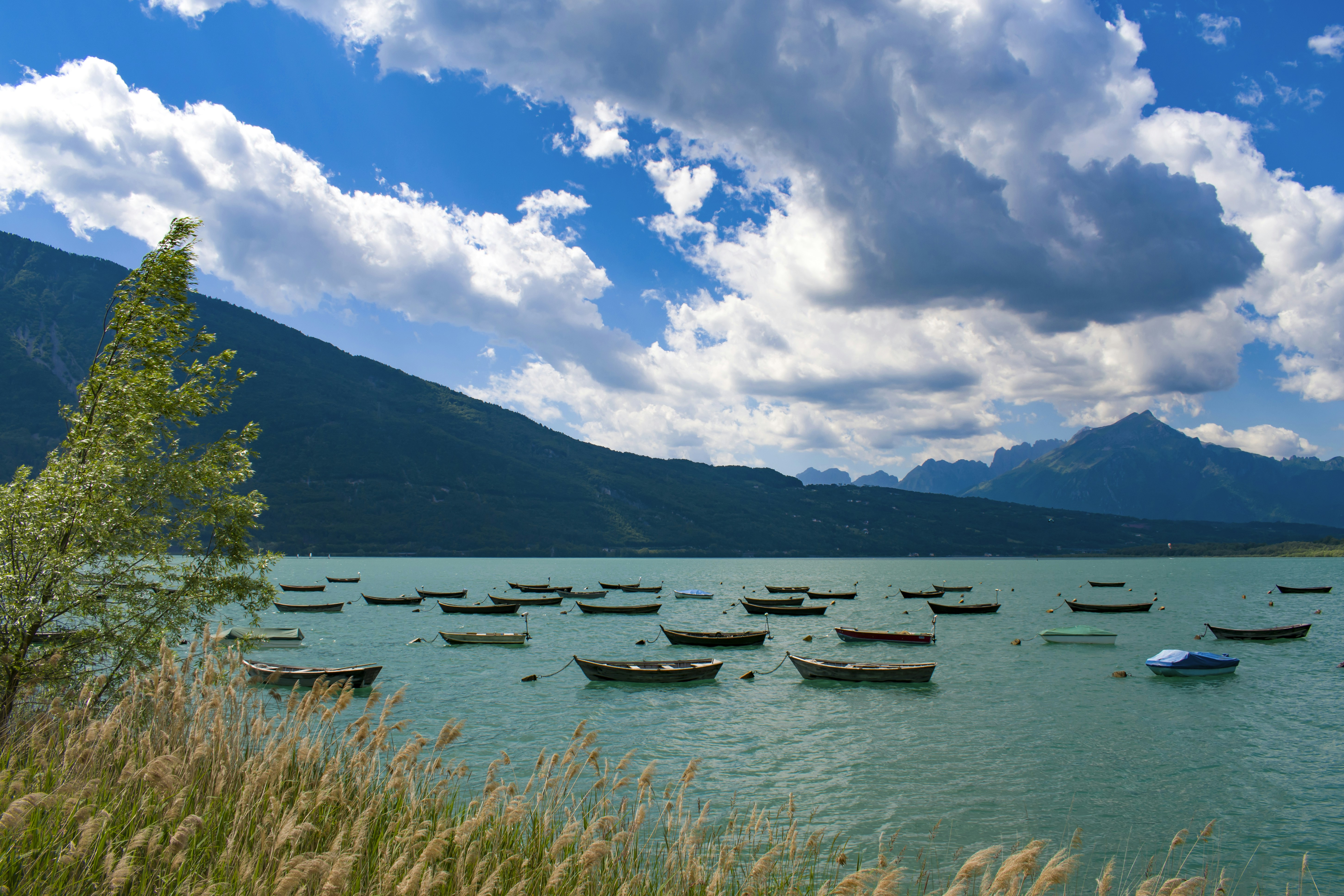Rowboats dotting a vivid turquoise lake beneath a sky filled with dramatic clouds and distant mountains.