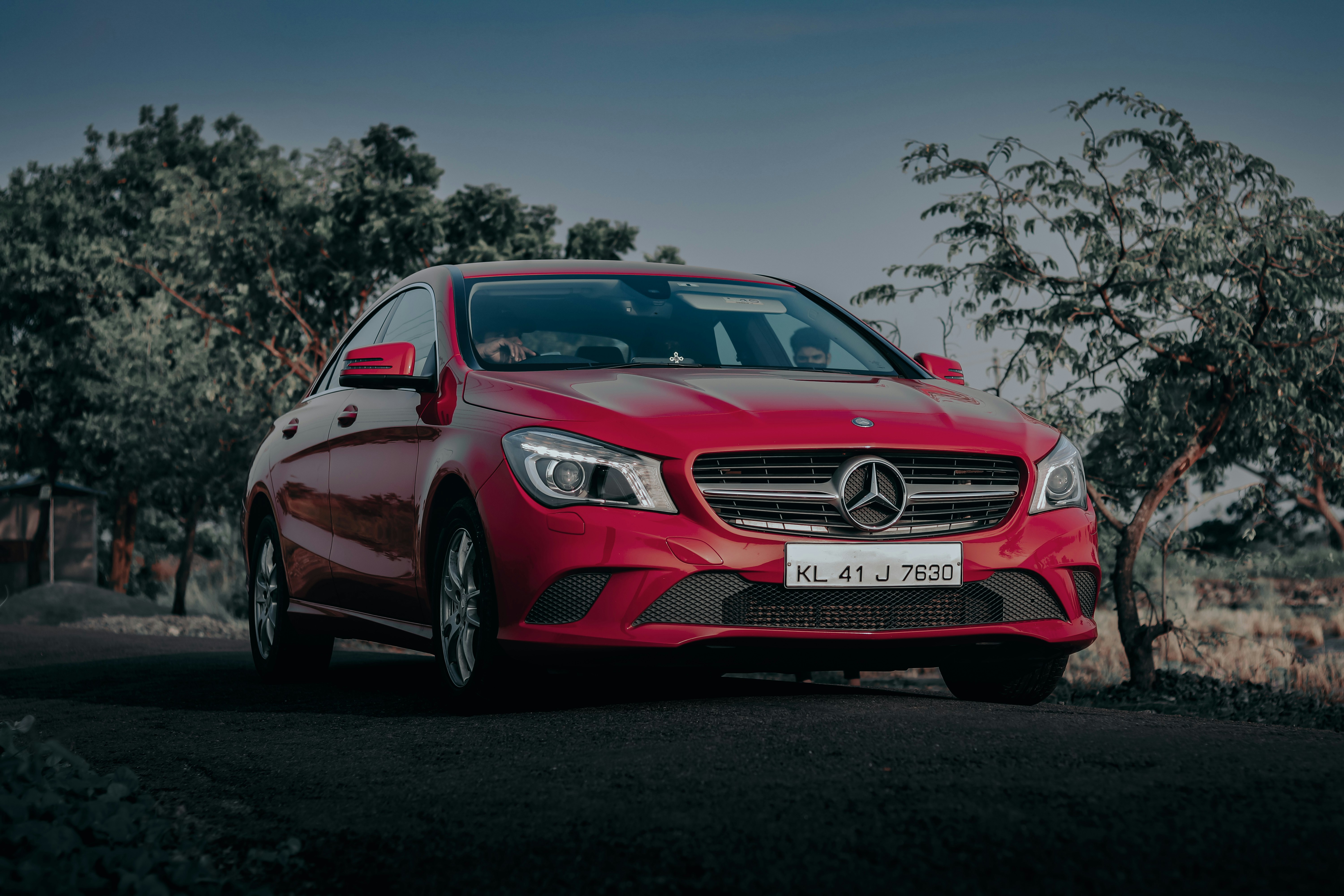 Red Mercedes-Benz parked on a rural road with trees and a dusky sky in the background.