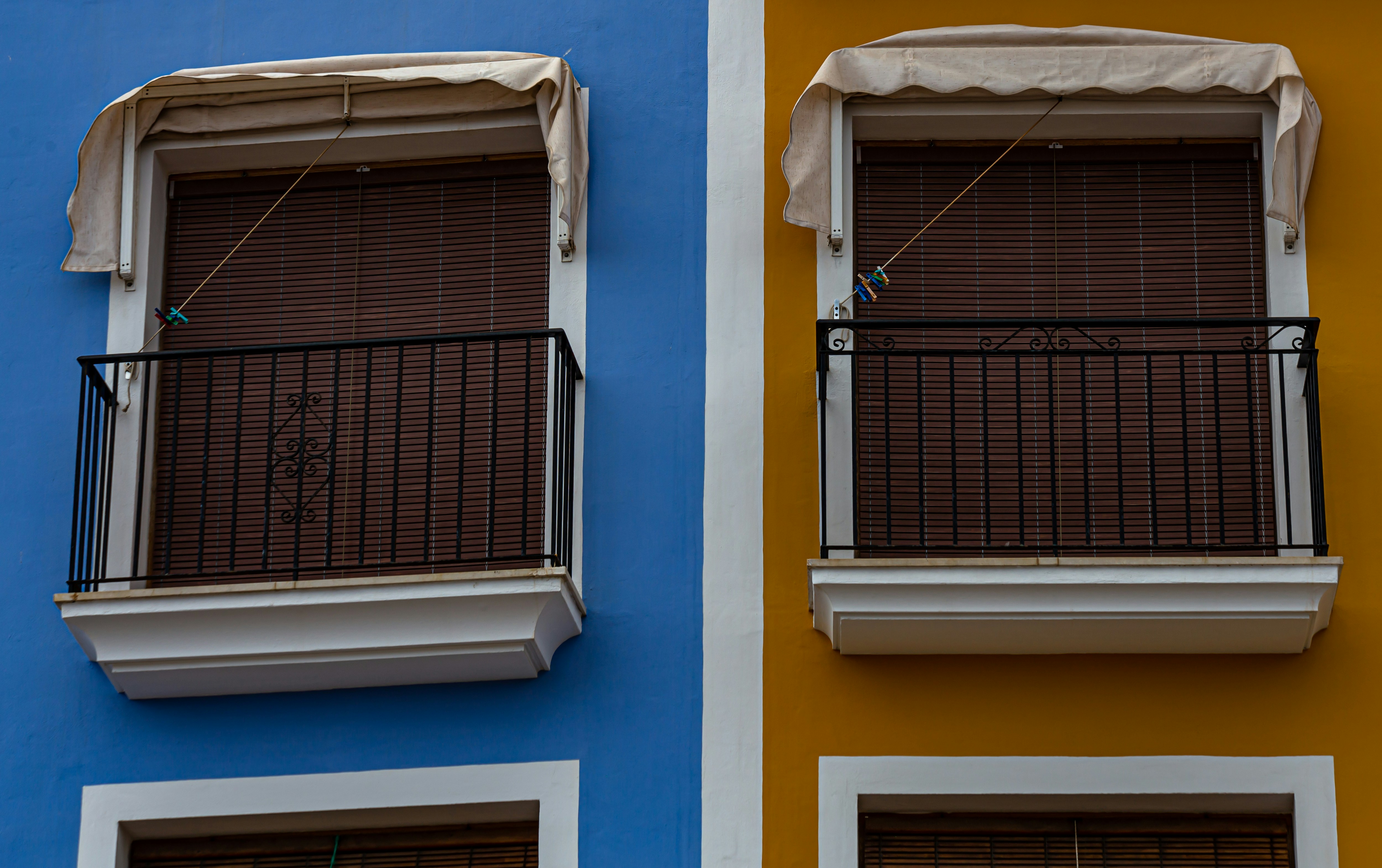 Two balconies with wooden shutters framed by vibrant blue and yellow walls, showcasing architectural symmetry.