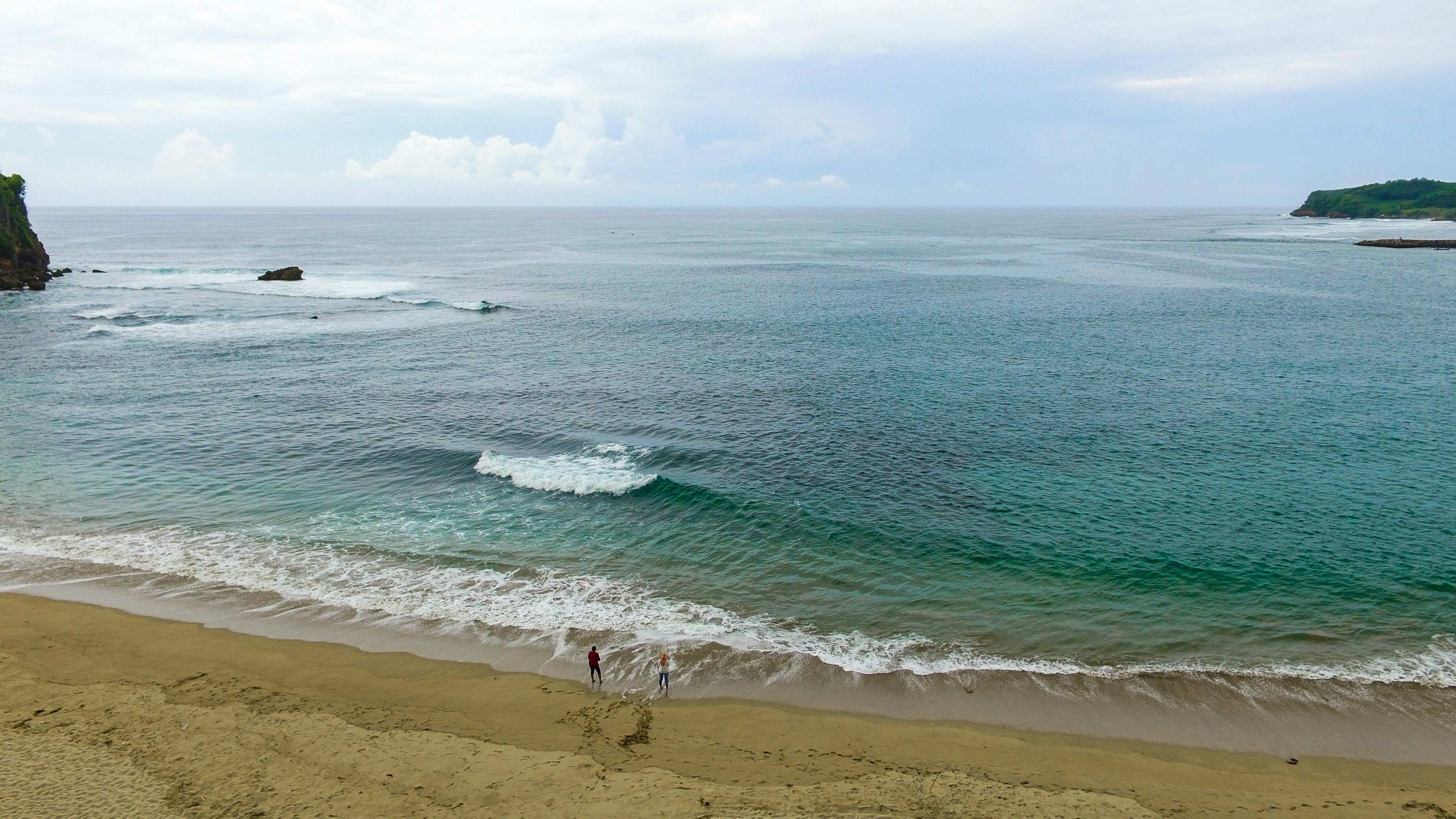 Expansive beach with gentle waves rolling onto the sandy shore under a cloudy sky.