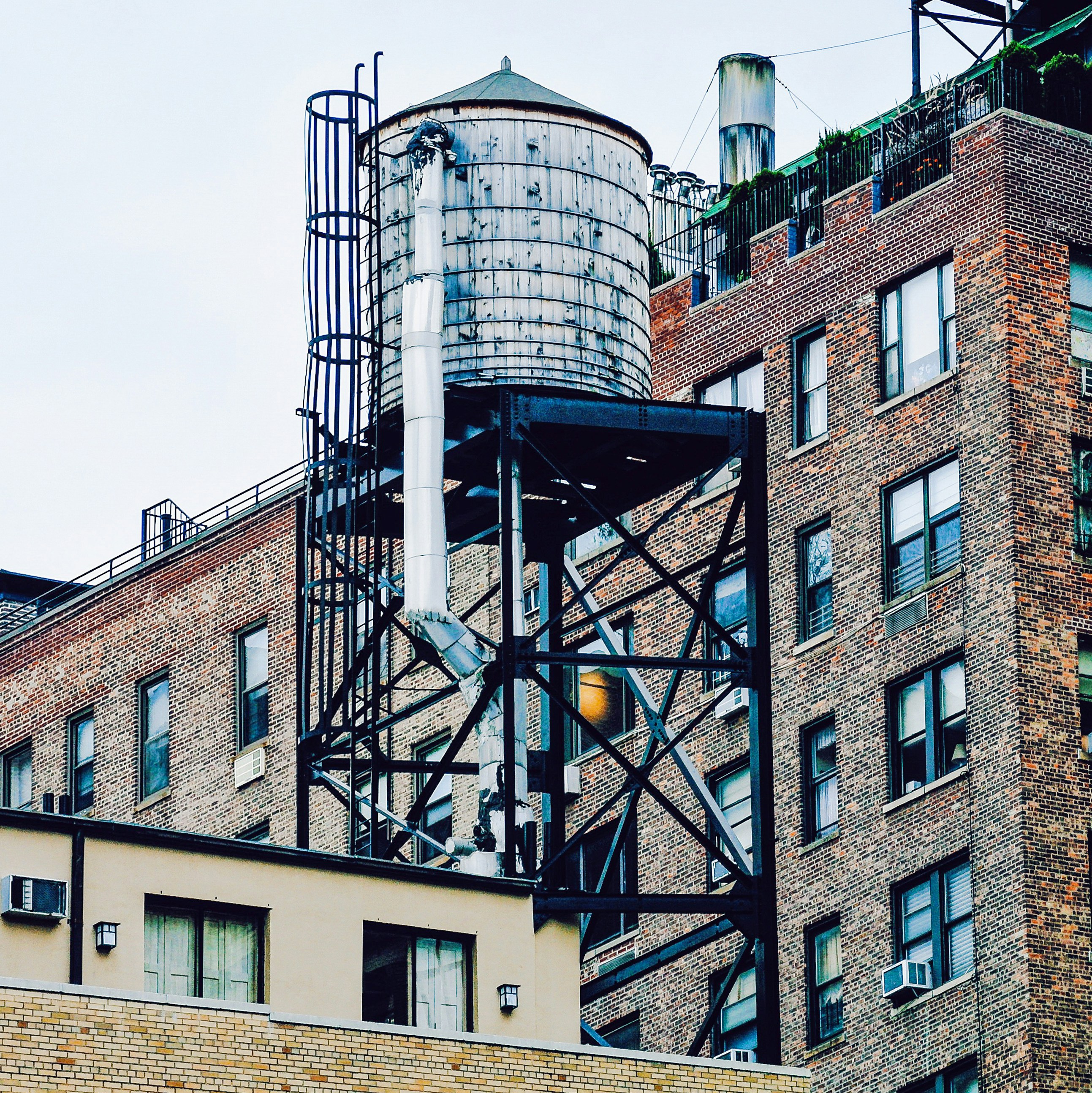 Weathered water tower on a rooftop, surrounded by brick buildings, showcasing urban architecture and industrial design.
