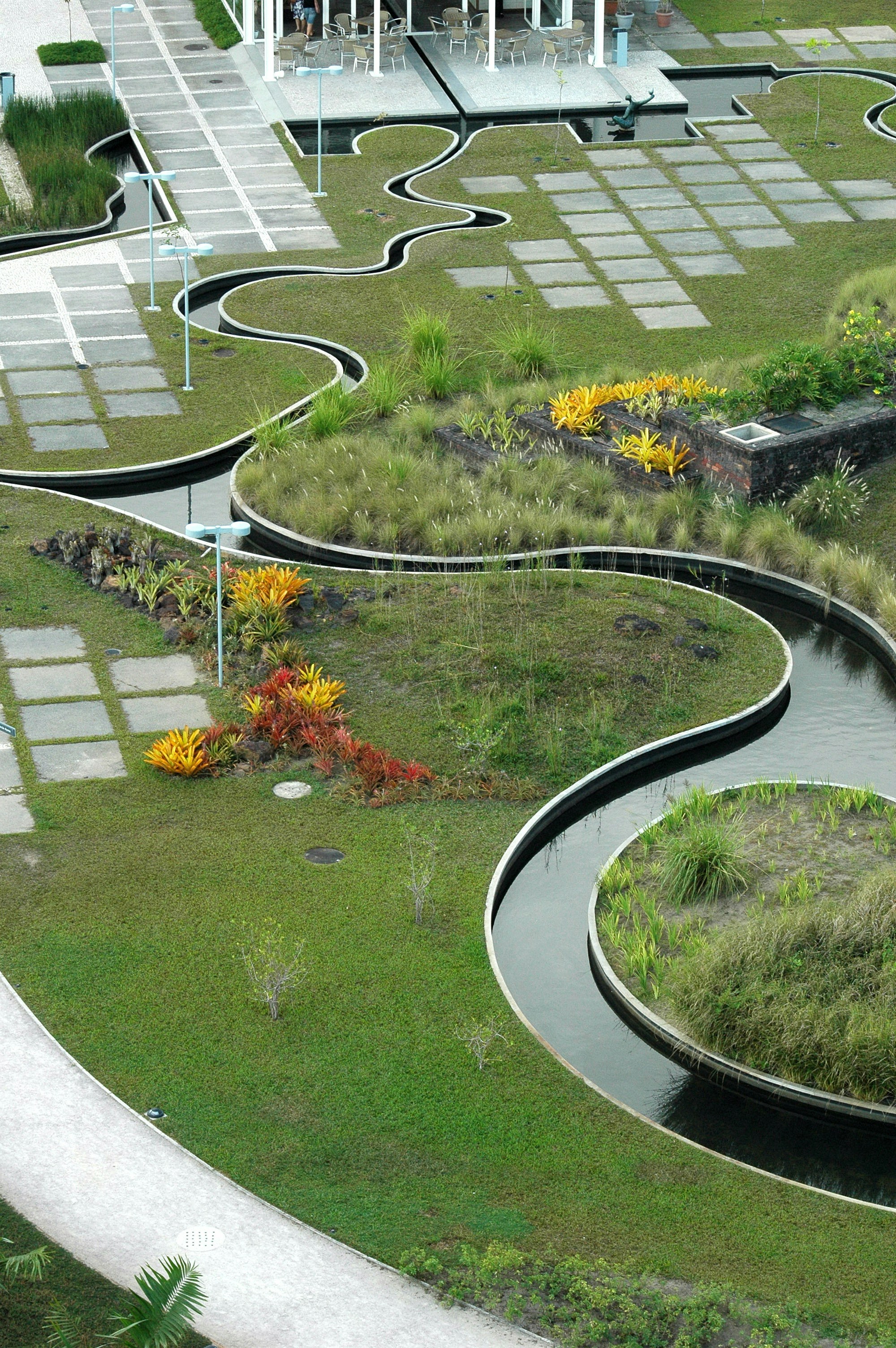 Aerial photograph of a modern garden featuring winding water channels, grassy islands, and geometric stone paths.