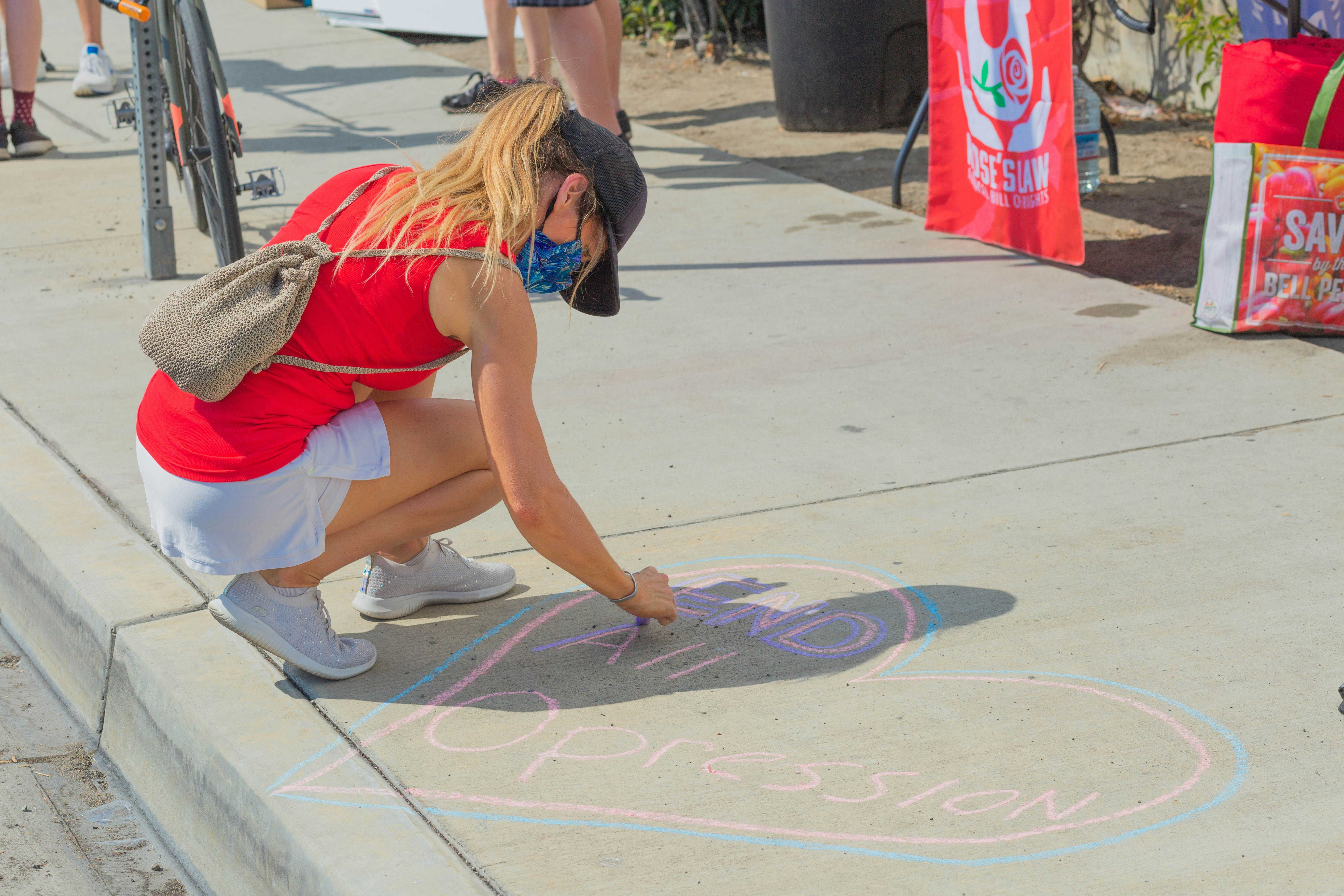 Individual creating a chalk drawing on the sidewalk with a message of solidarity. The scene captures community activism and personal expression.