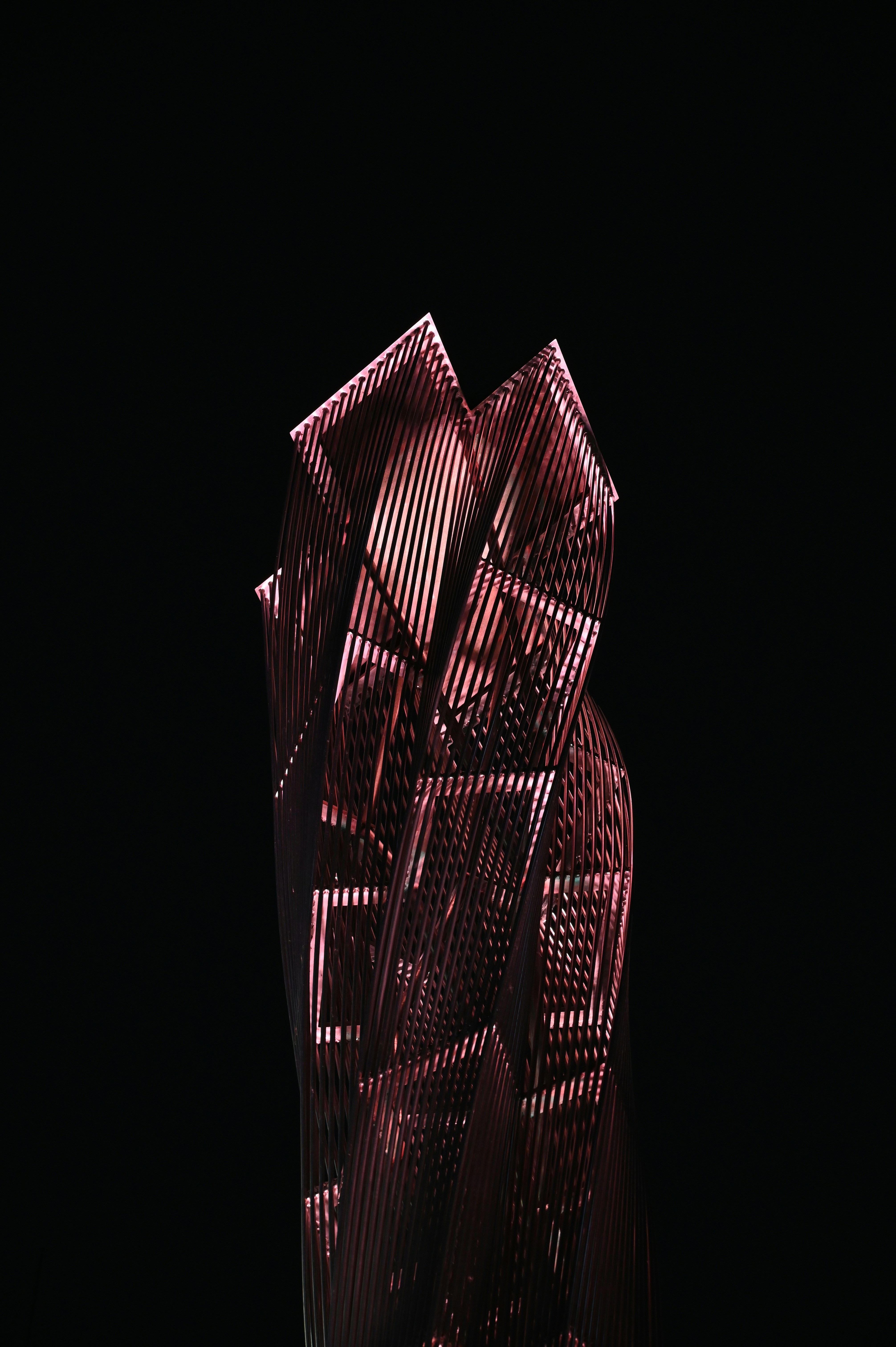 Abstract sculpture with intricate lines and layers, illuminated against a dark backdrop. The interplay of light and shadow enhances its dynamic form.