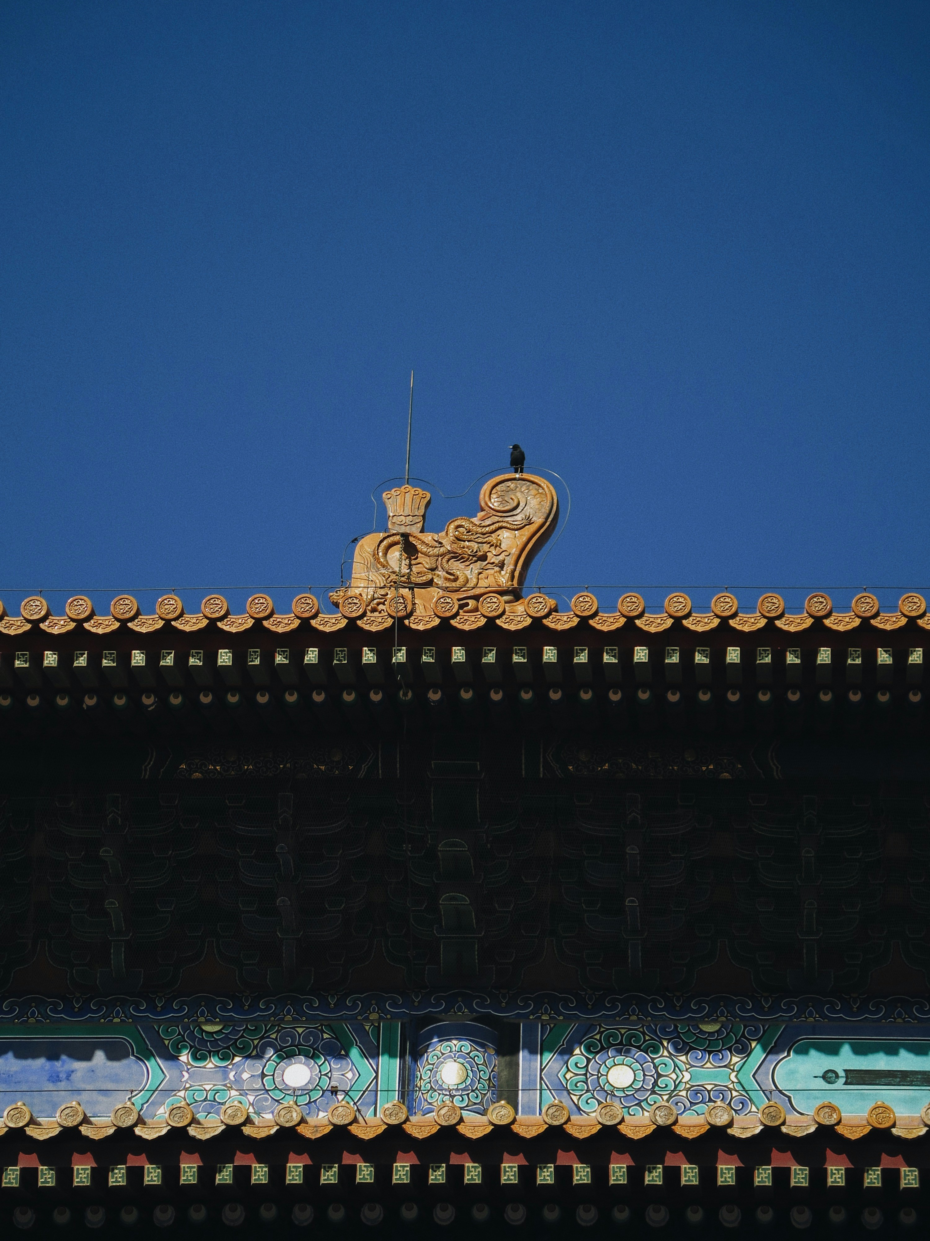 Ornate dragon crest atop a traditional roof against a deep blue sky; intricate eaves and tile patterns visible below.