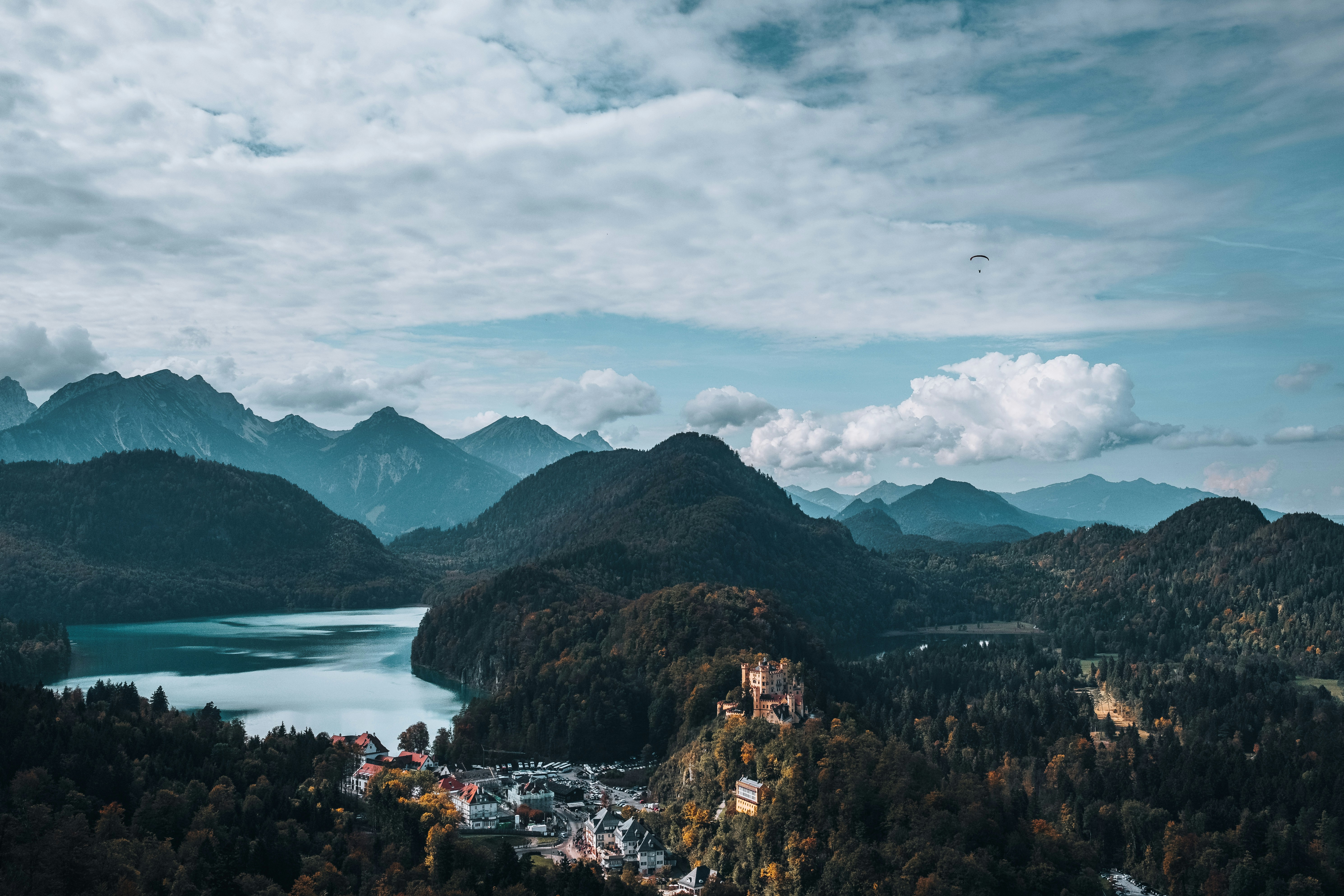 Castle nestled among forested mountains and a serene lake under a dramatic sky.