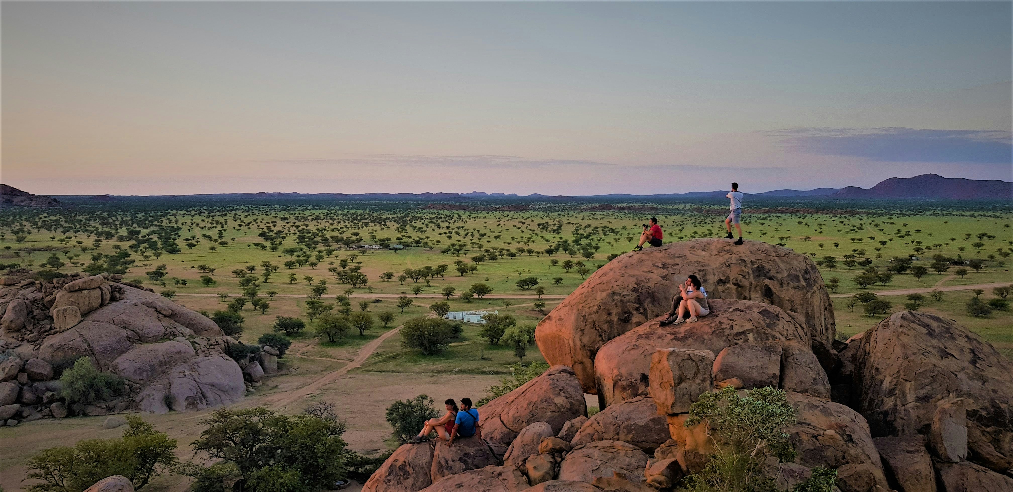 Sunset at Damarland (Namibia) | people on brown rock formation near green grass field during daytime