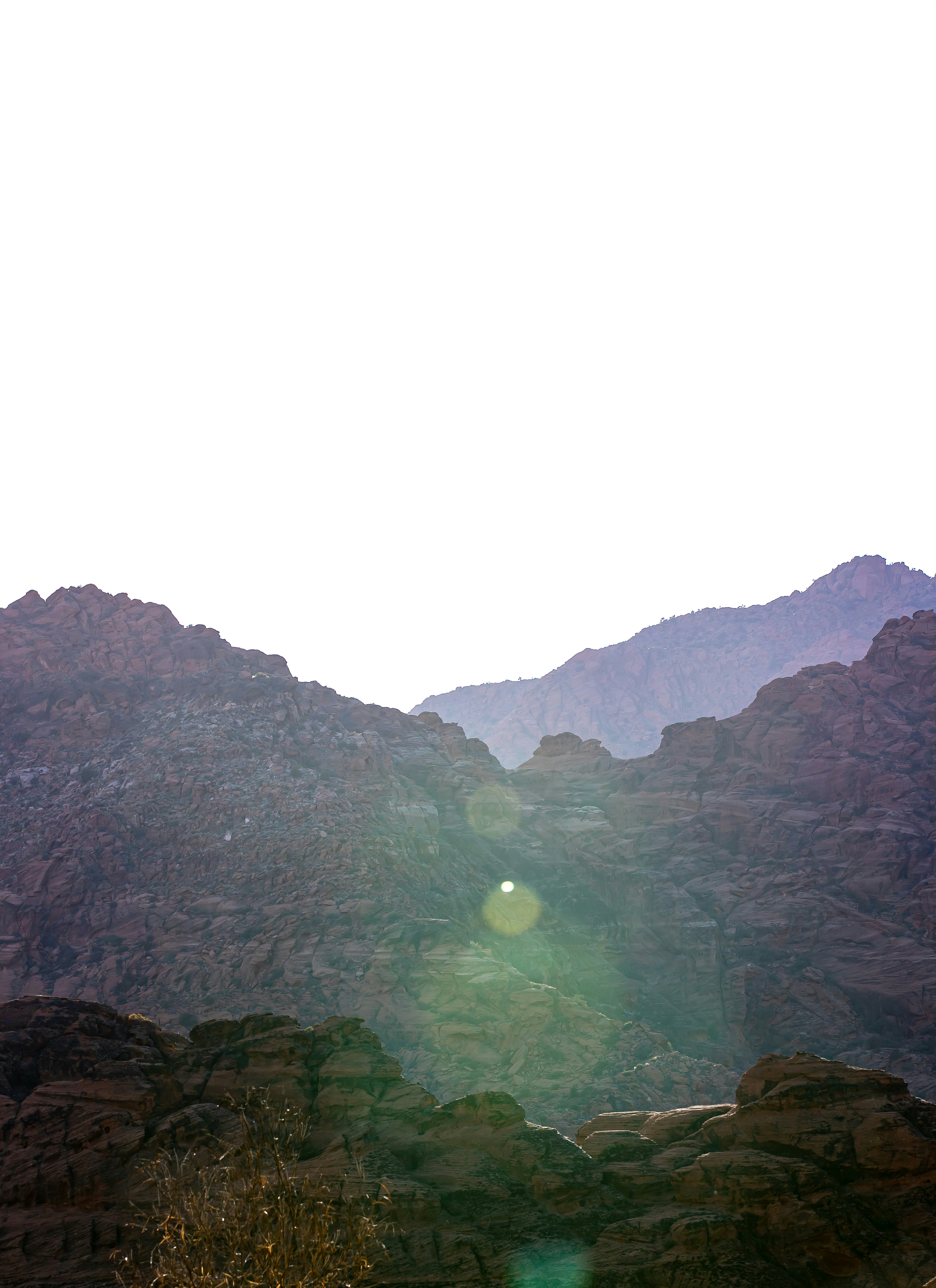 Mountains shrouded in soft light, revealing textured rock formations under a bright sky.