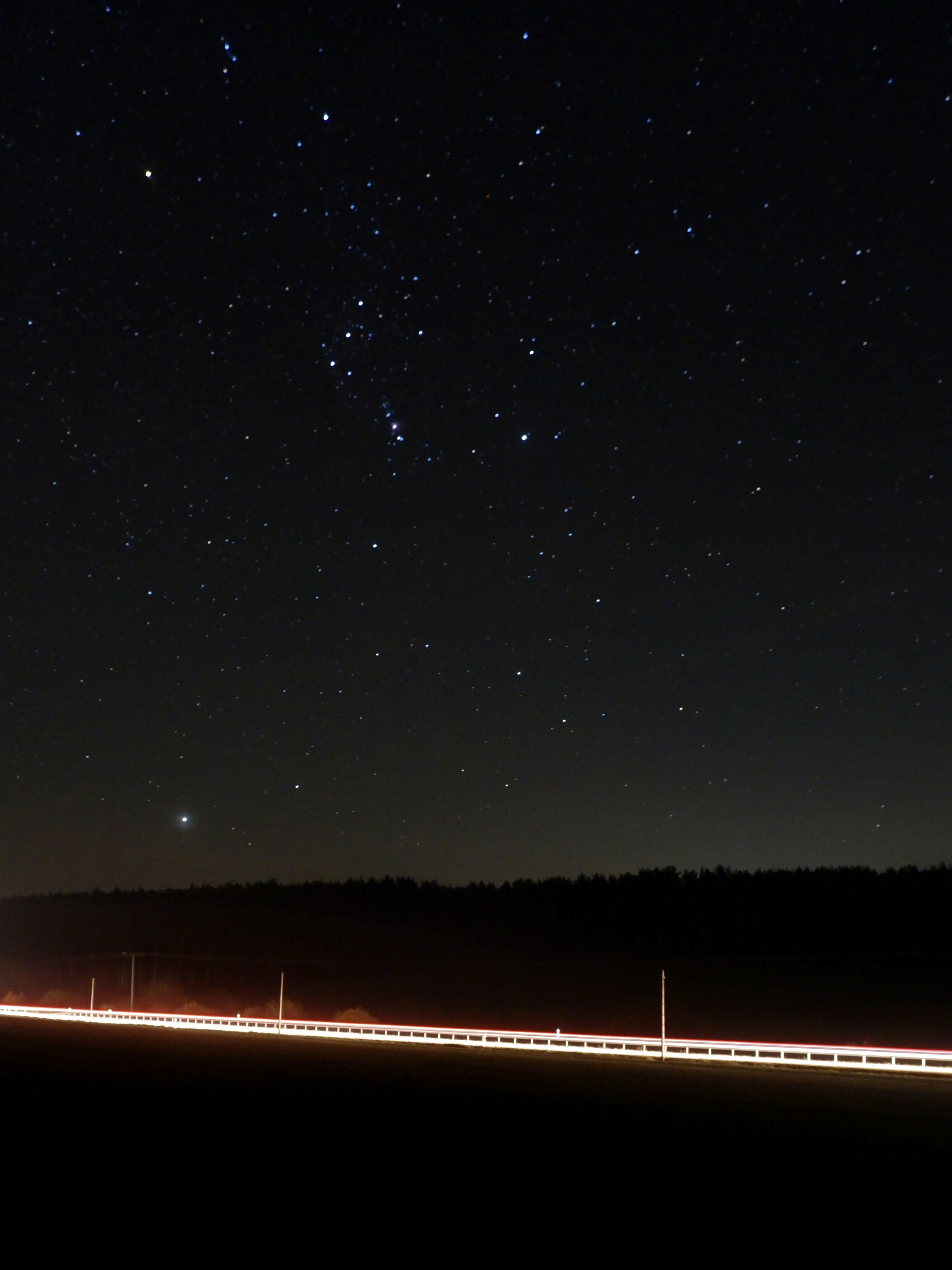 Long exposure photograph capturing the night sky filled with stars and a streak of light from passing vehicles on an open road.