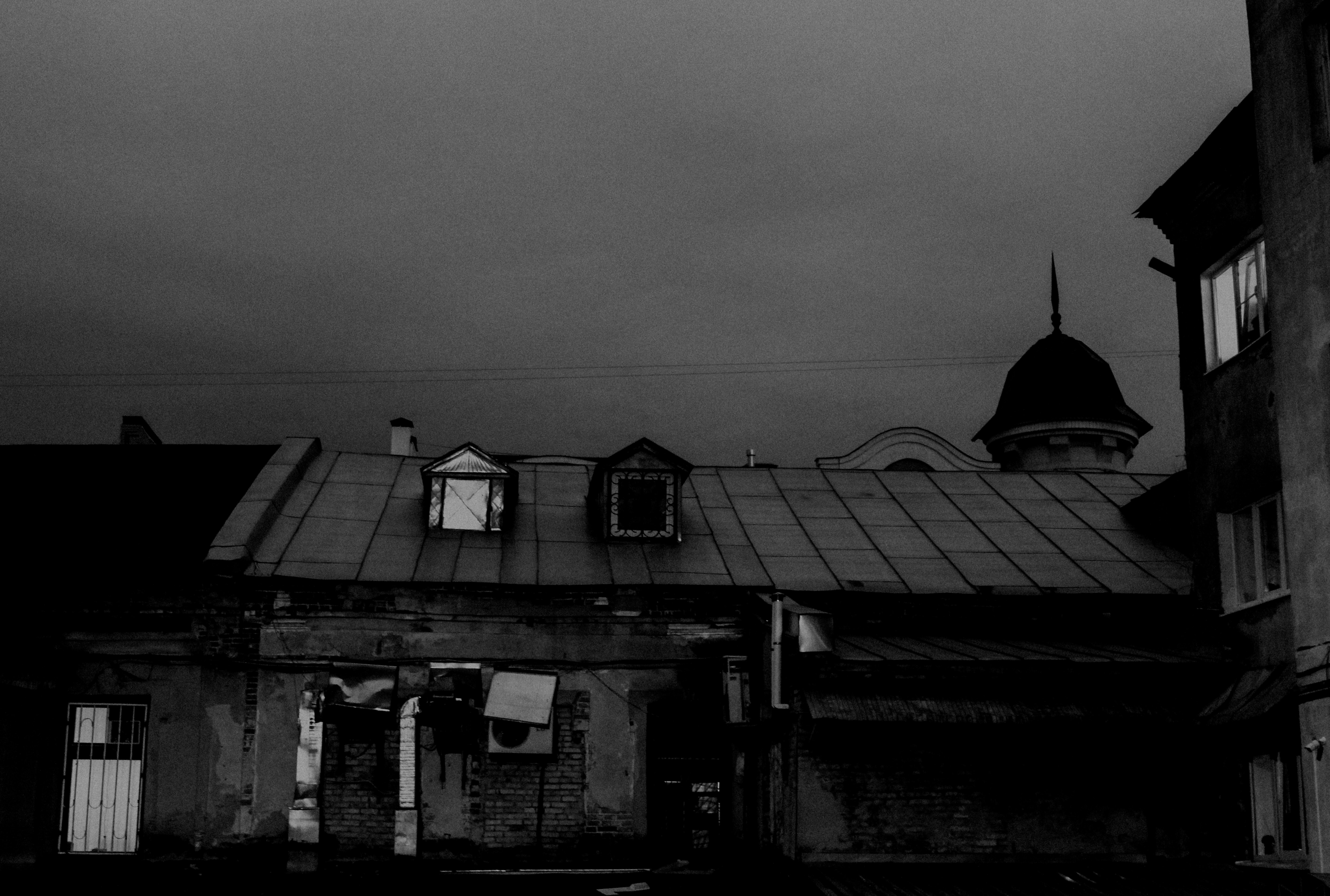 Abandoned rooftops under a moody sky, featuring a prominent spire and scattered windows reflecting the dim light.