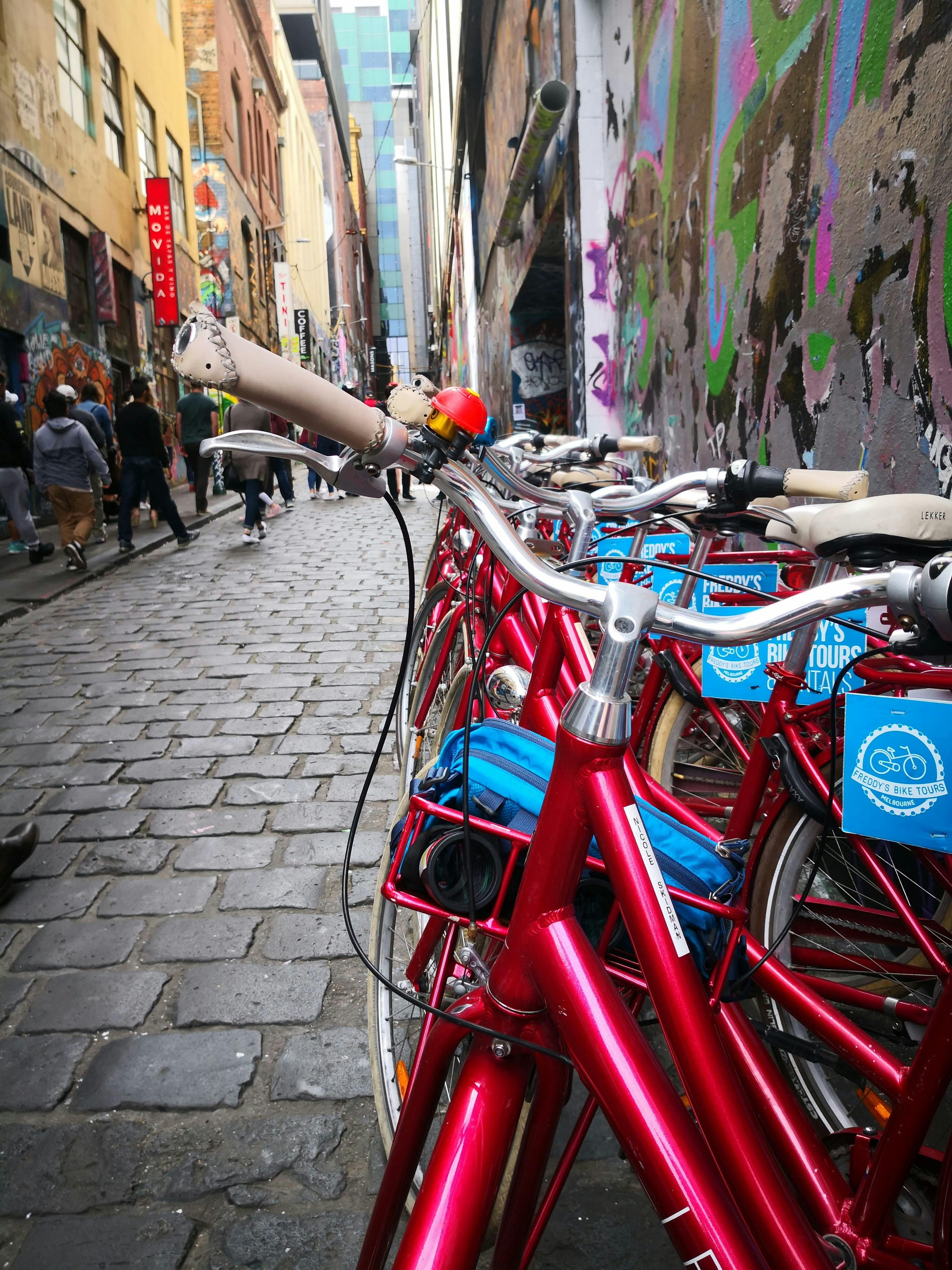 Row of vibrant red bicycles parked along a graffiti-adorned alleyway, inviting exploration in a bustling urban landscape.