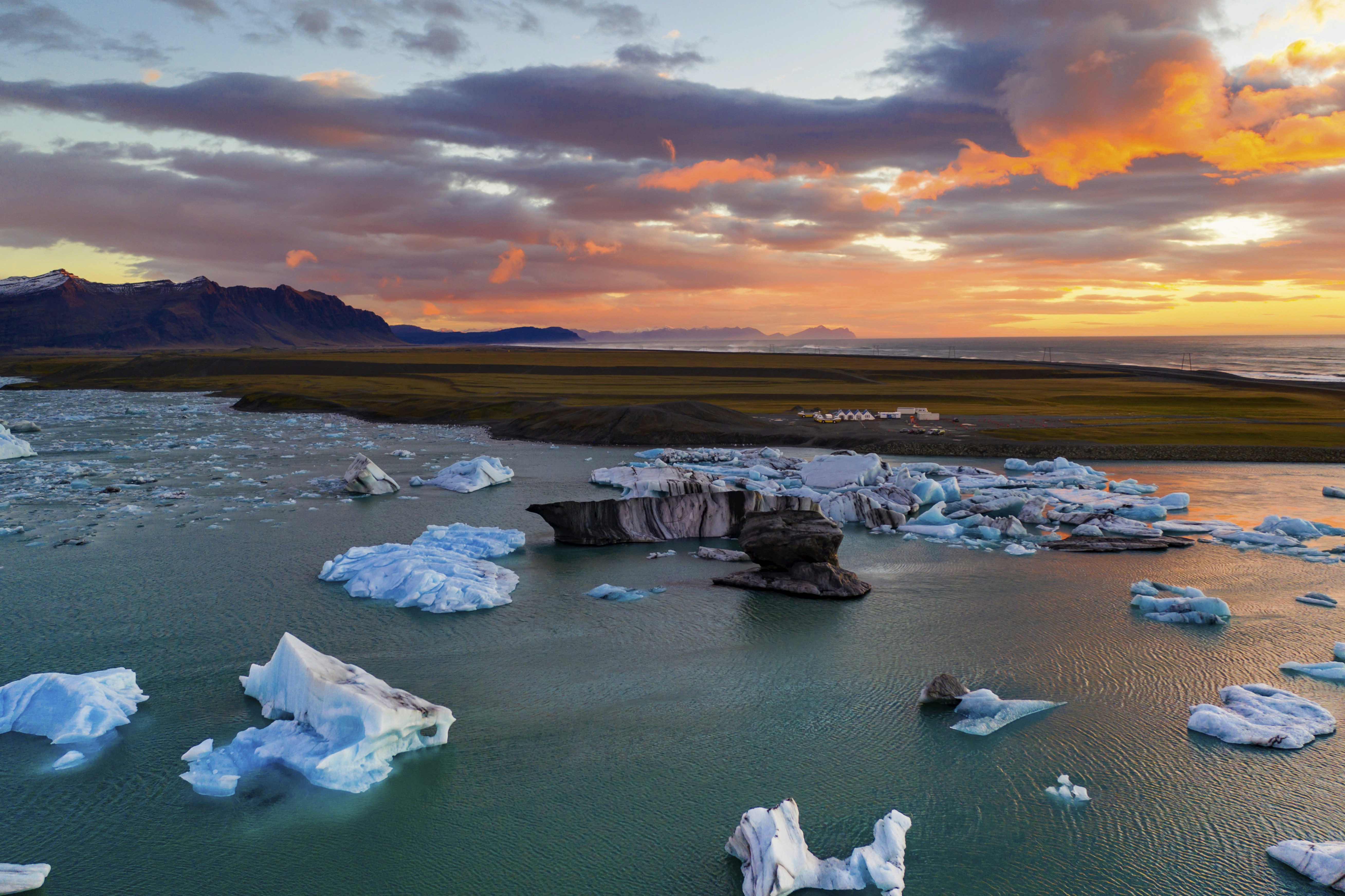 Icy shoreline at sunset: jagged blue icebergs drift on calm waters