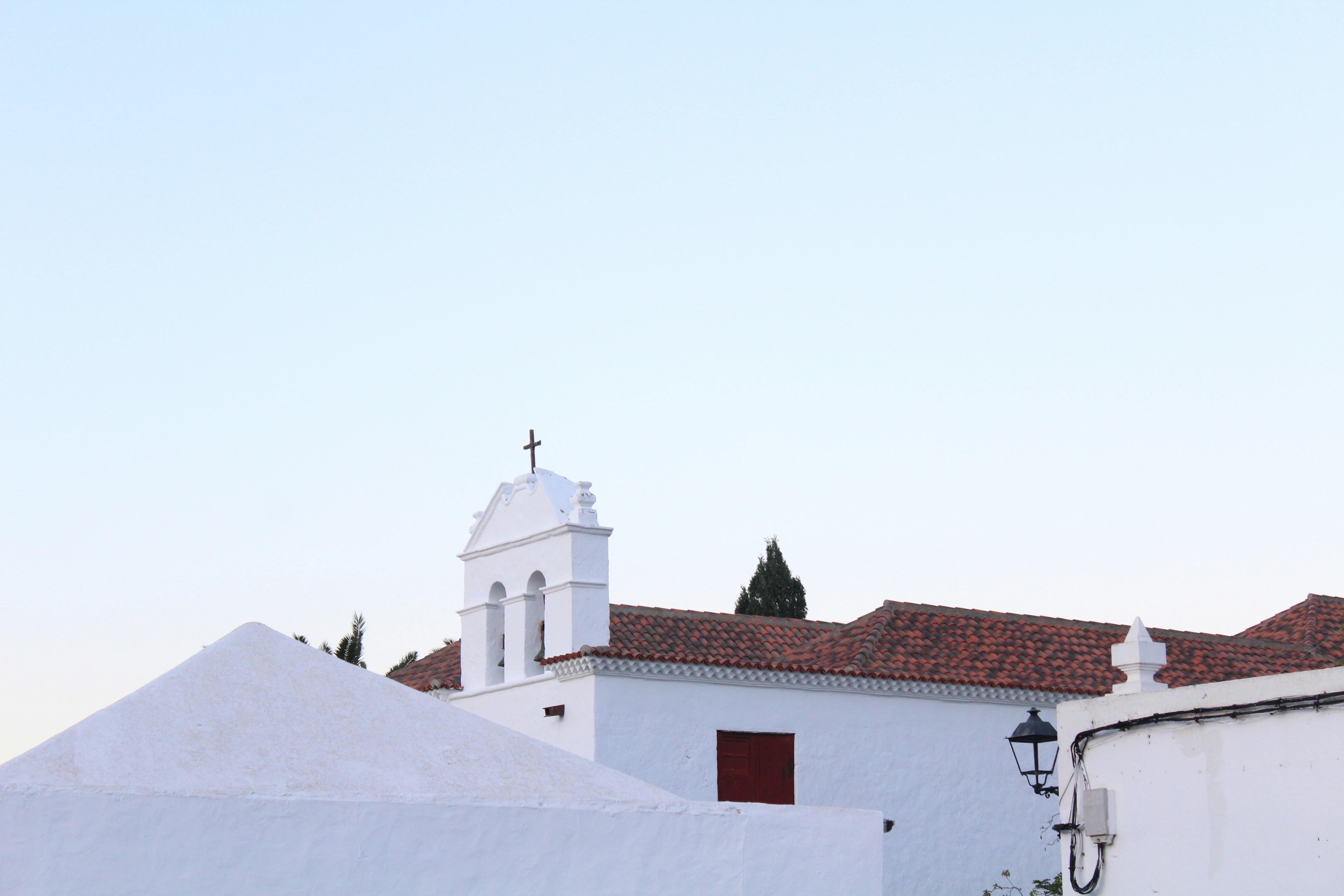 White concrete chapel with a cross, set against a clear daytime sky.