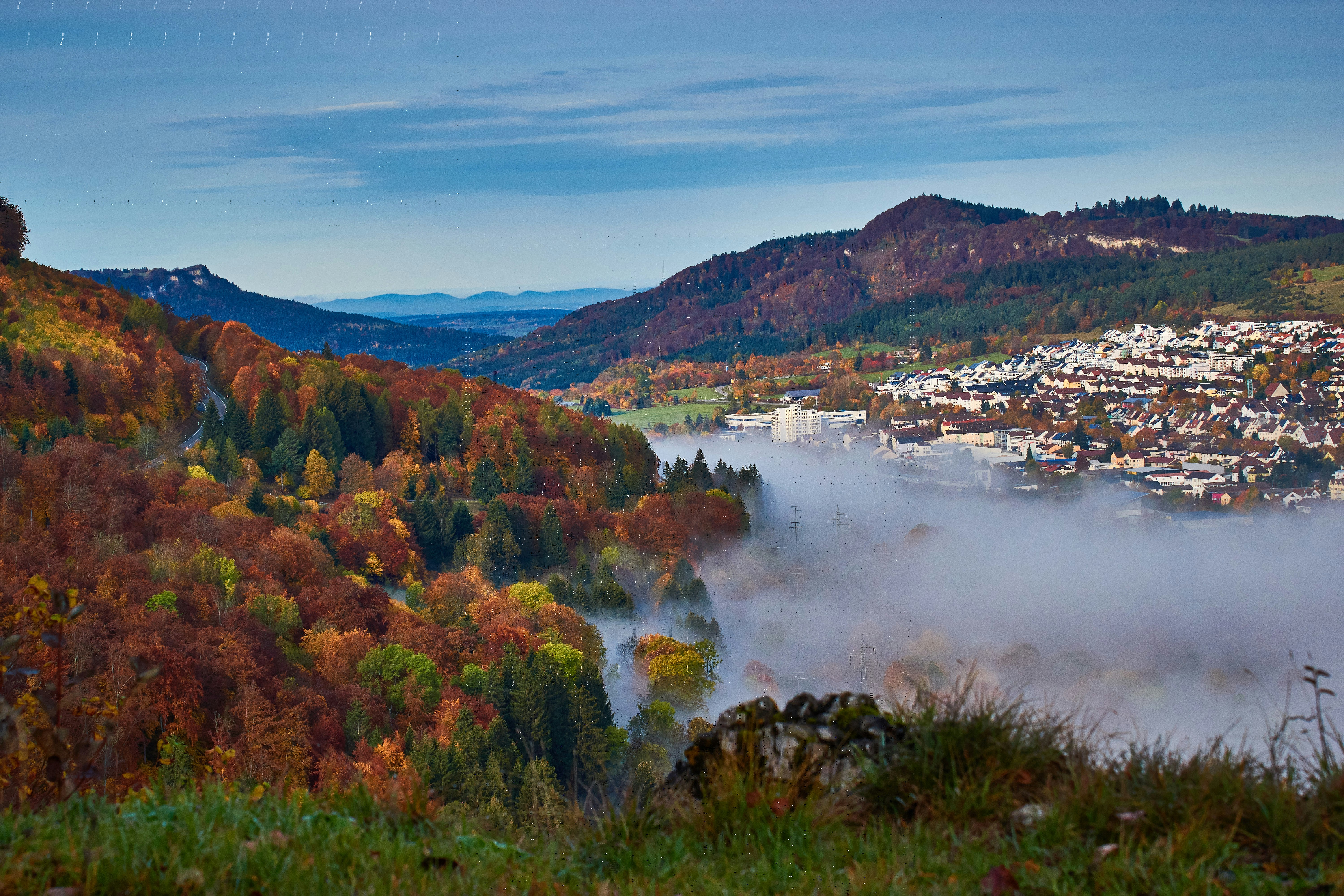 Mist over the autumn valley: town tucked between colorful hills