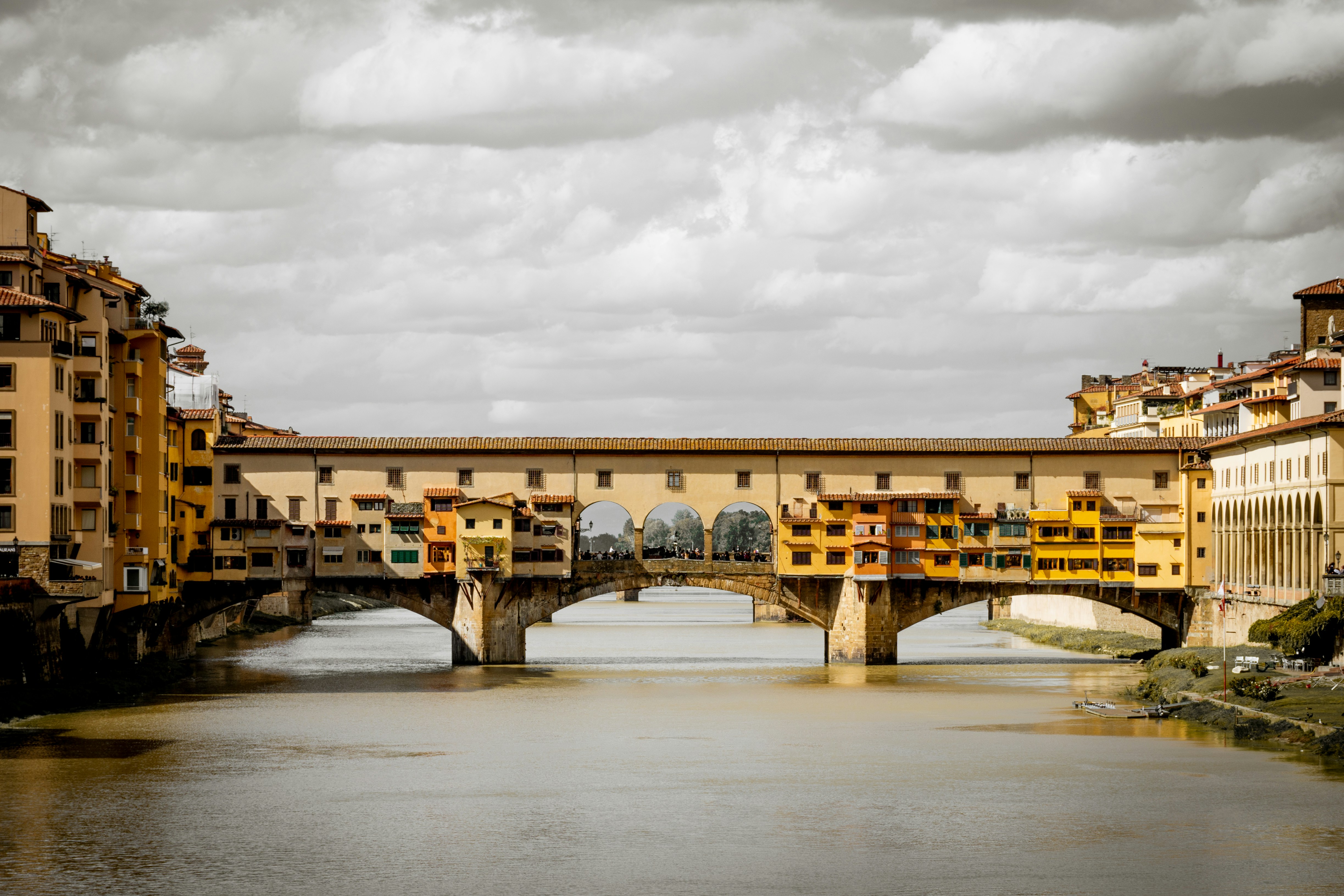 Historic stone bridge spanning a river, surrounded by classic architecture under a cloud-filled sky.