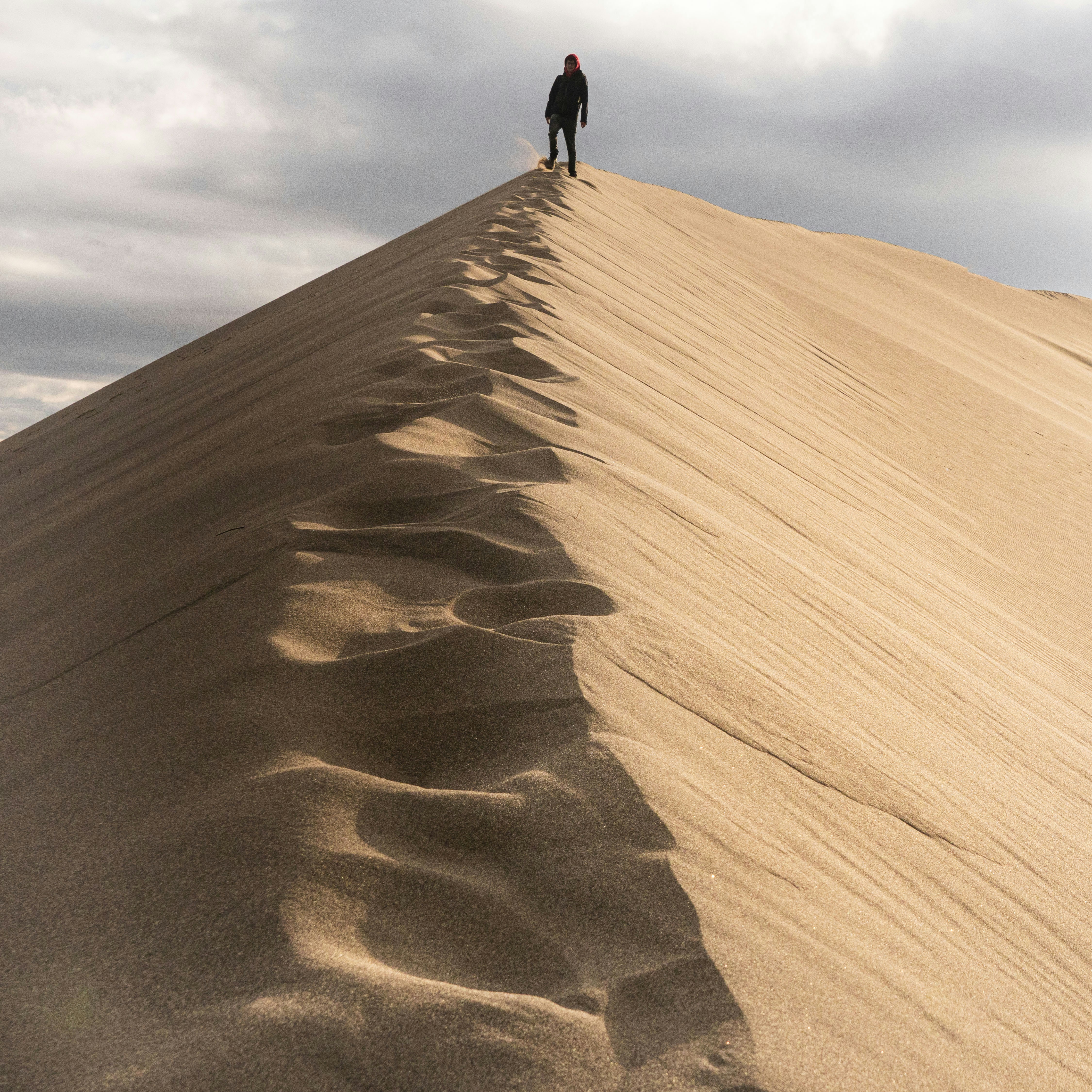 Crestline Solitude: A lone climber crowns a windswept desert dune