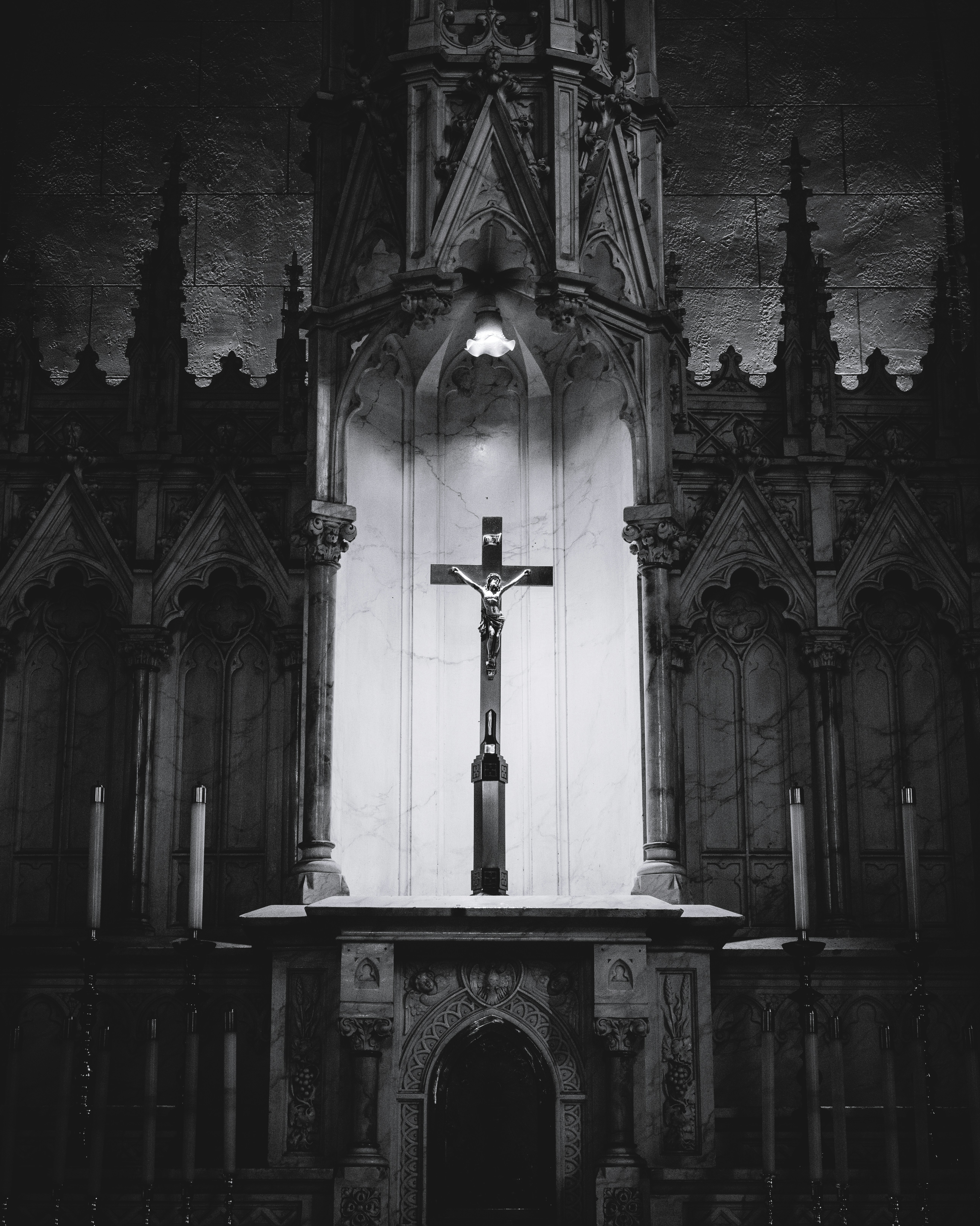 Intricate gothic altar with a crucifix illuminated under a single light in a grayscale church setting.