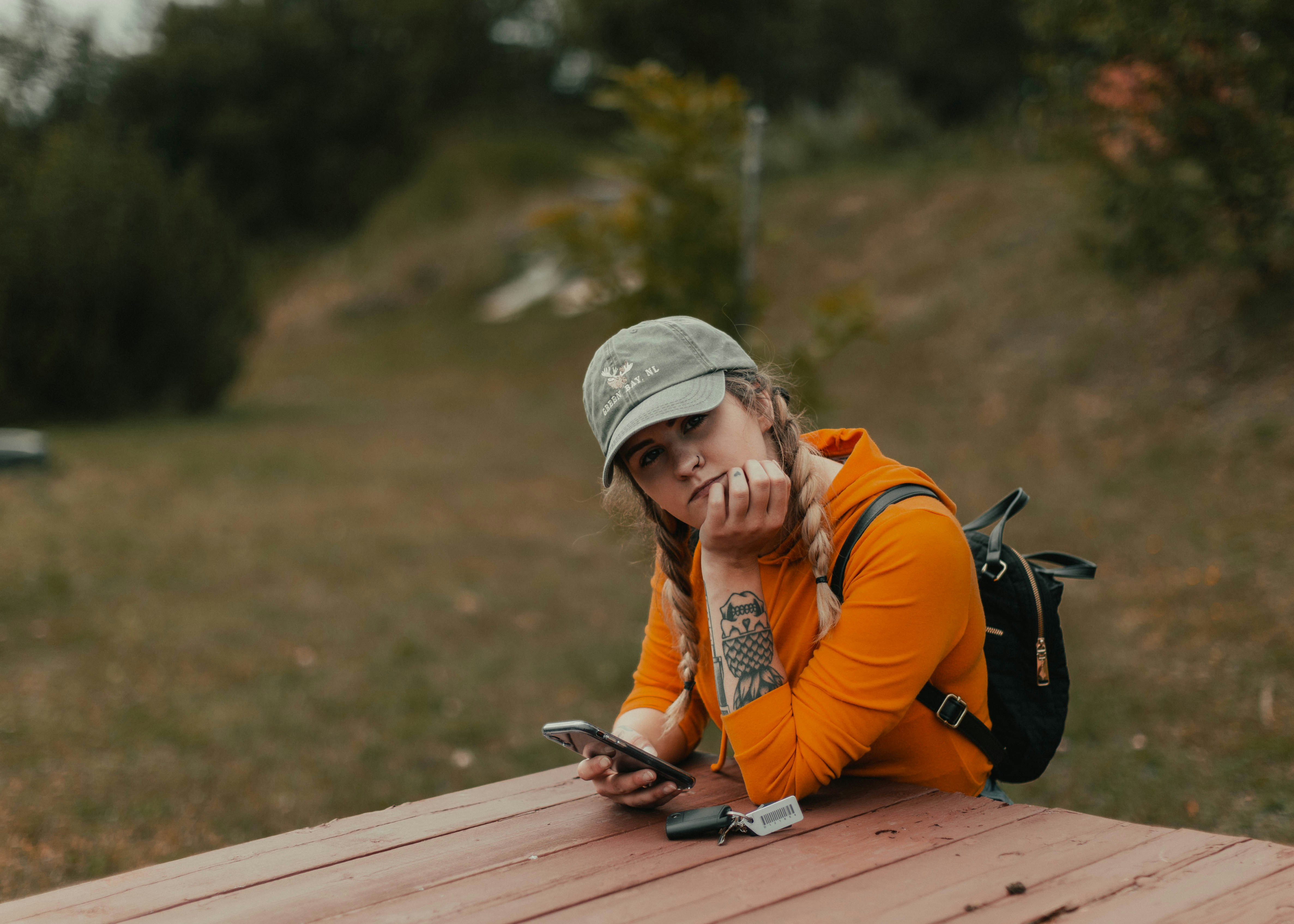Portrait at the Picnic Table: Tattooed Hands, Orange Hoodie, and a Quiet Moment outdoors