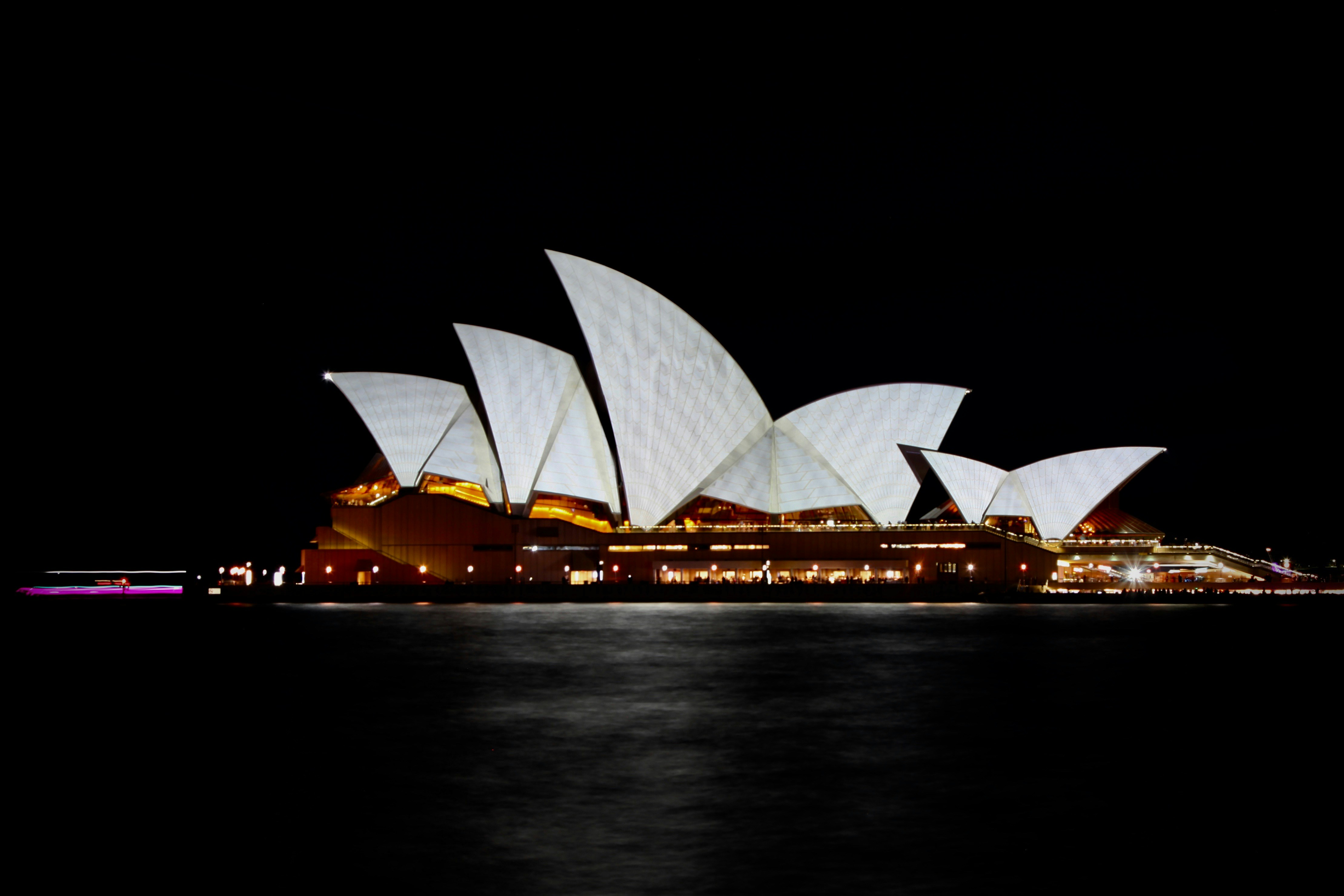 Sydney Opera House illuminated against the night sky with reflections on the harbor water.
