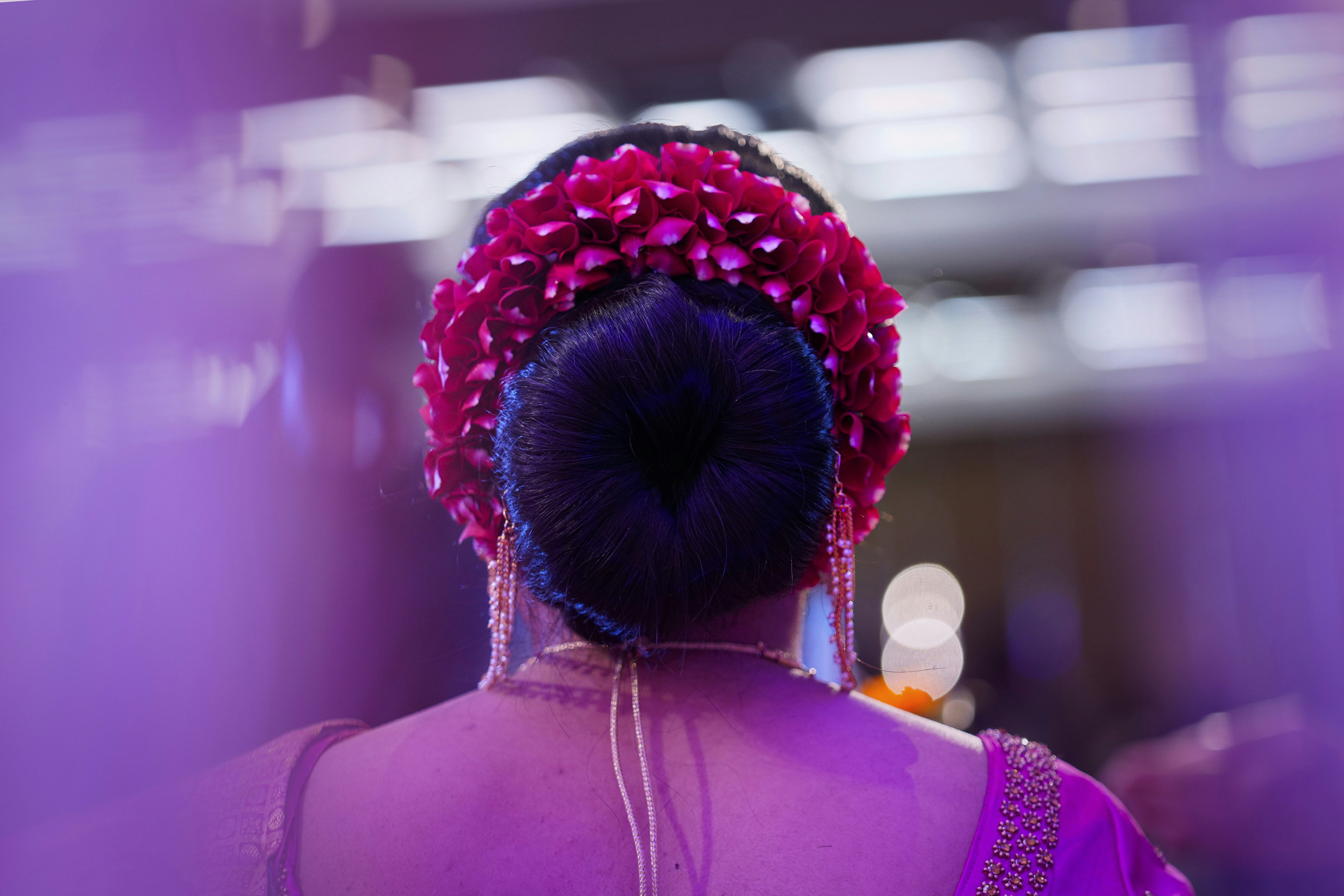 Back view of a woman adorned with a floral hairpiece and traditional attire, set against a softly blurred background. The scene captures the essence of cultural celebration.