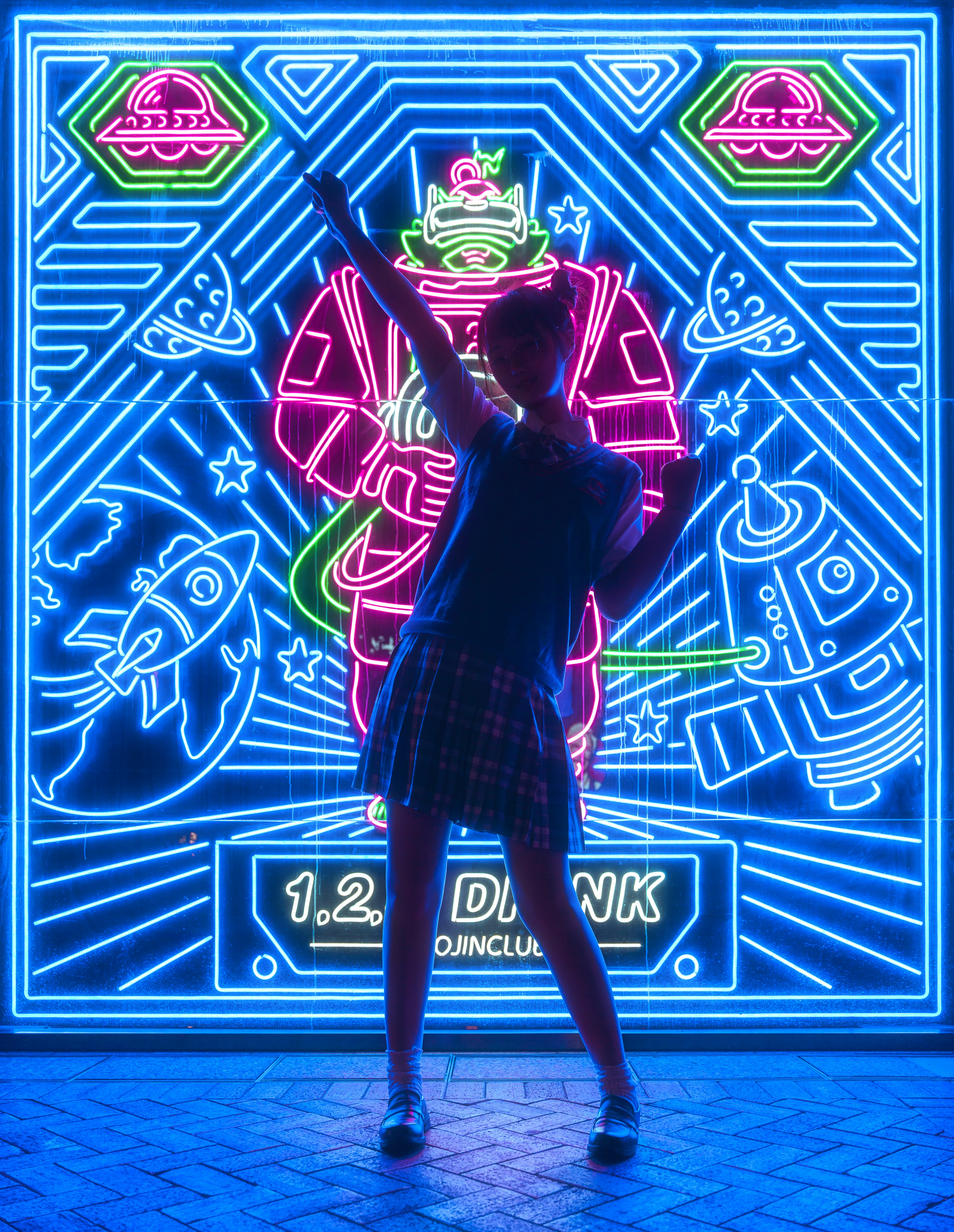 Silhouette of a dancer striking a pose in front of a vibrant neon mural featuring a whimsical alien theme. The colorful backdrop enhances the energetic atmosphere.