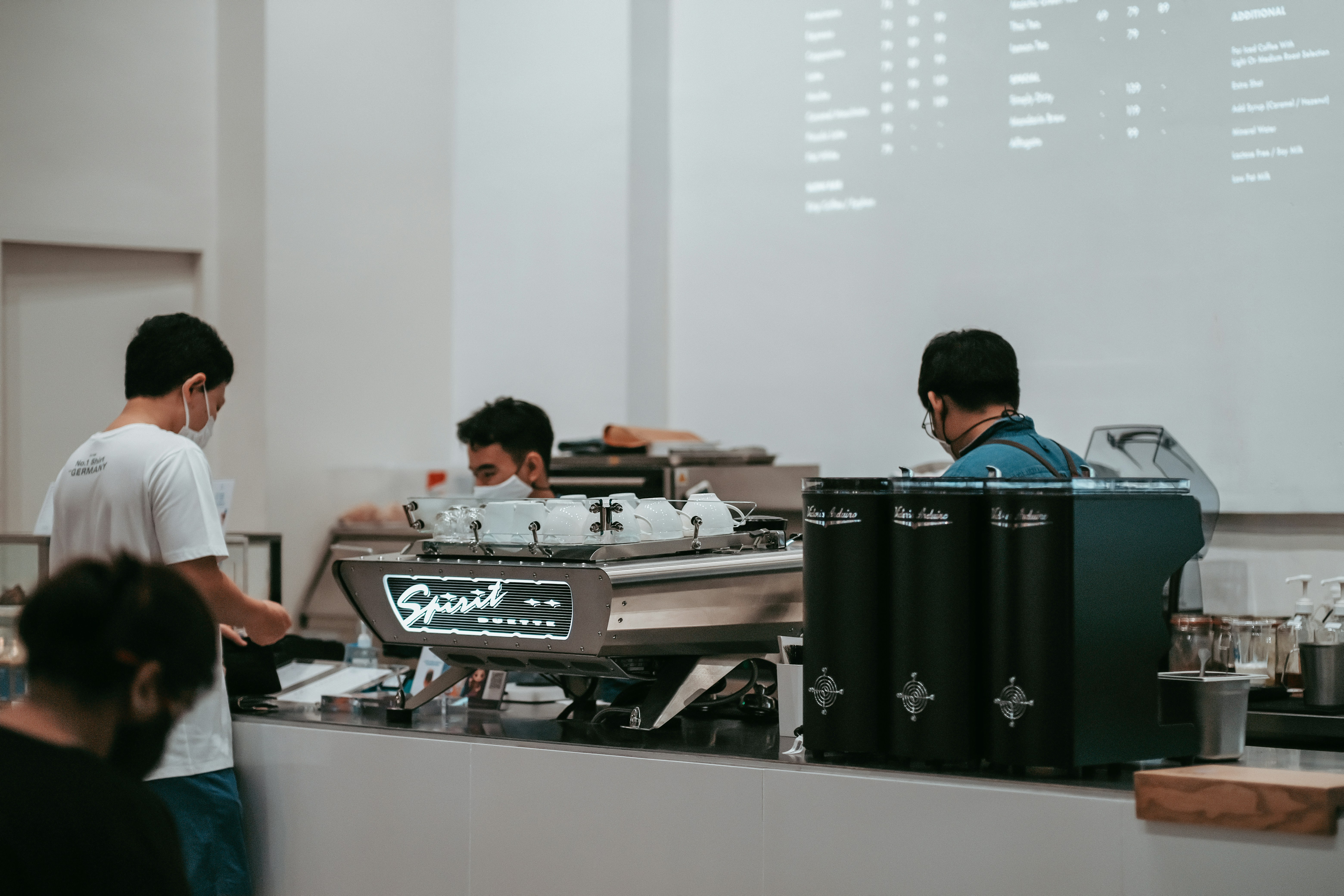 Baristas preparing coffee behind a modern espresso machine in a minimalist cafe setting.