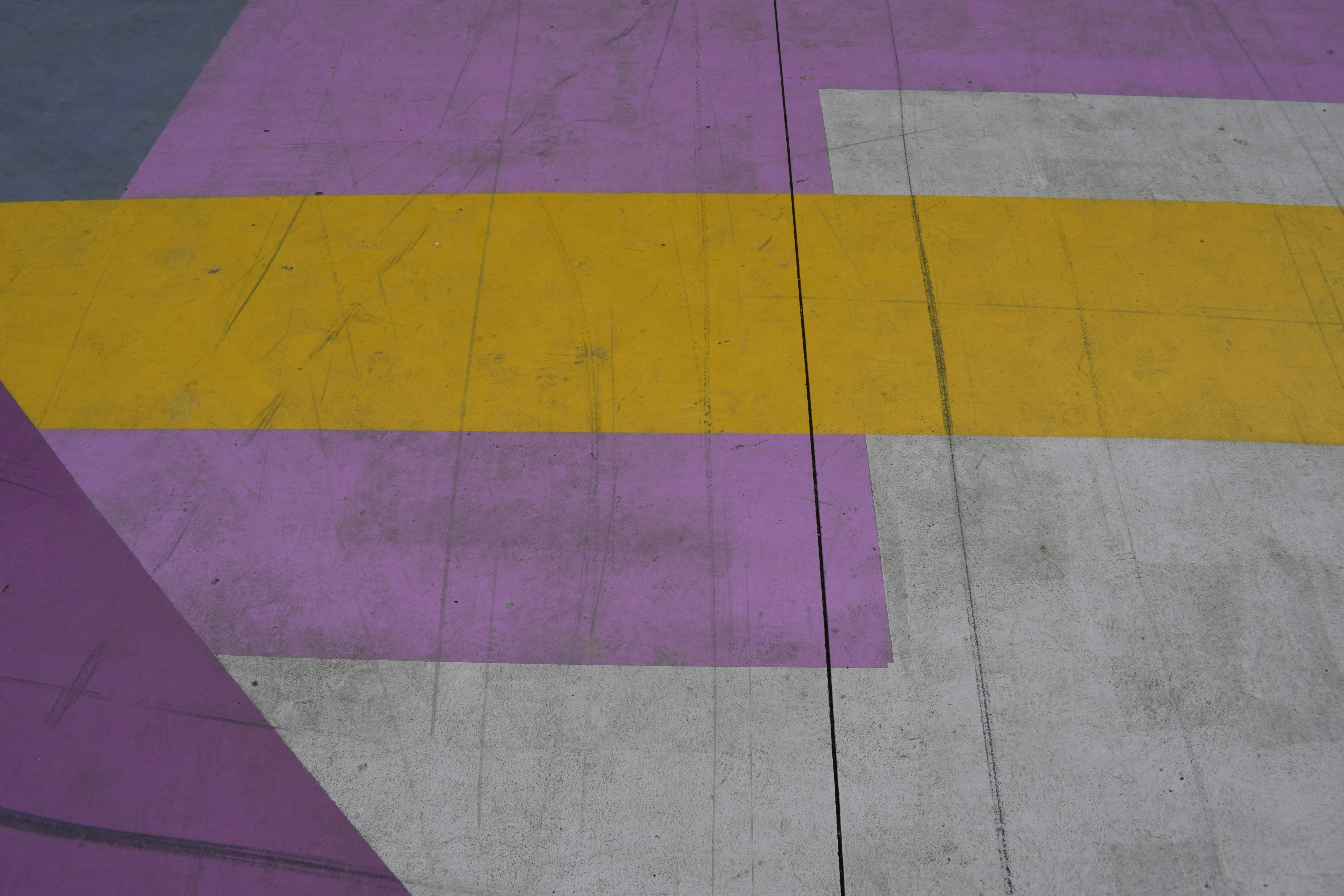 Geometric Crosswalk: Purple Stripes Meet a Yellow Line on Concrete