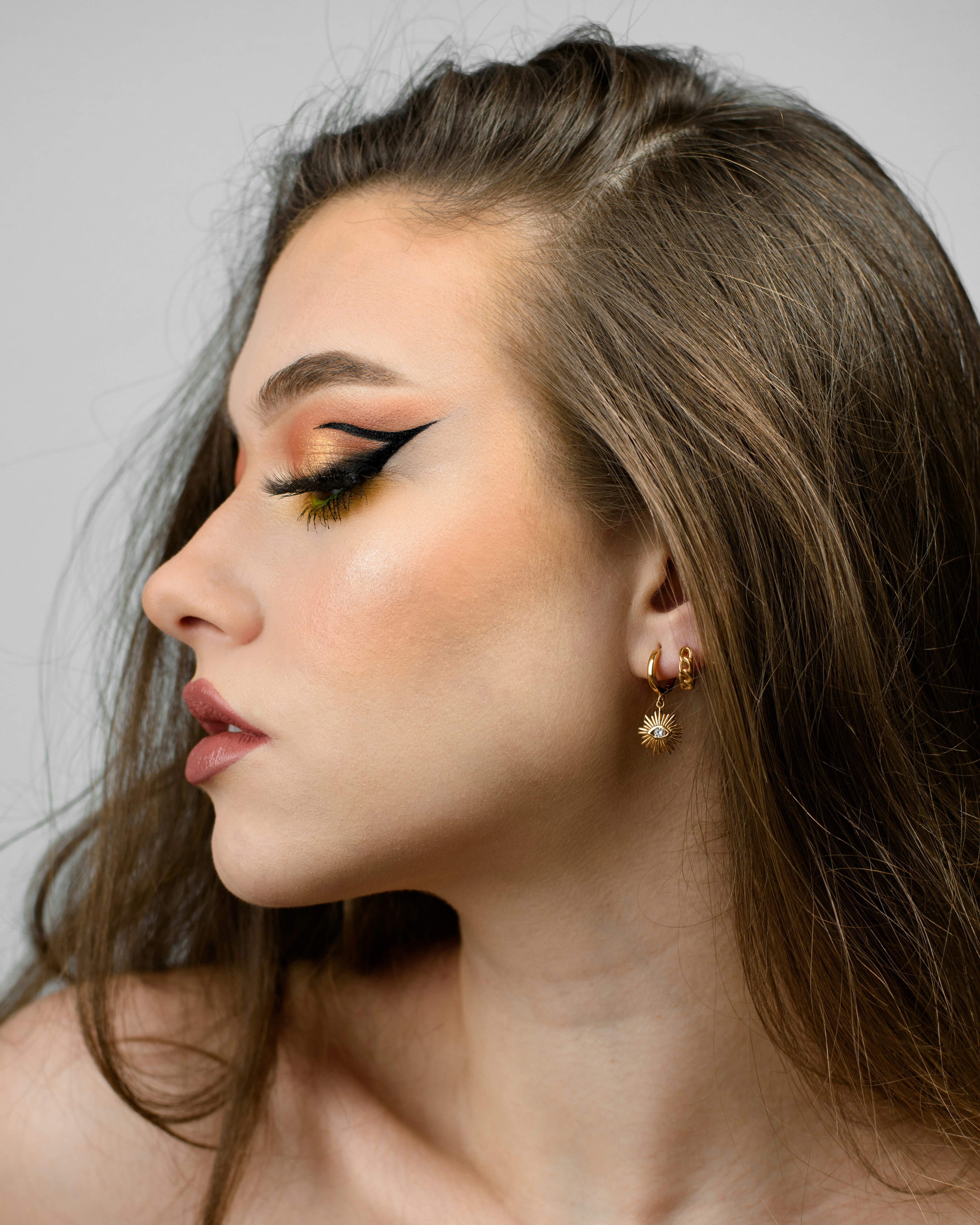 Profile shot of a model showcasing bold makeup and stylish earrings against a neutral background.