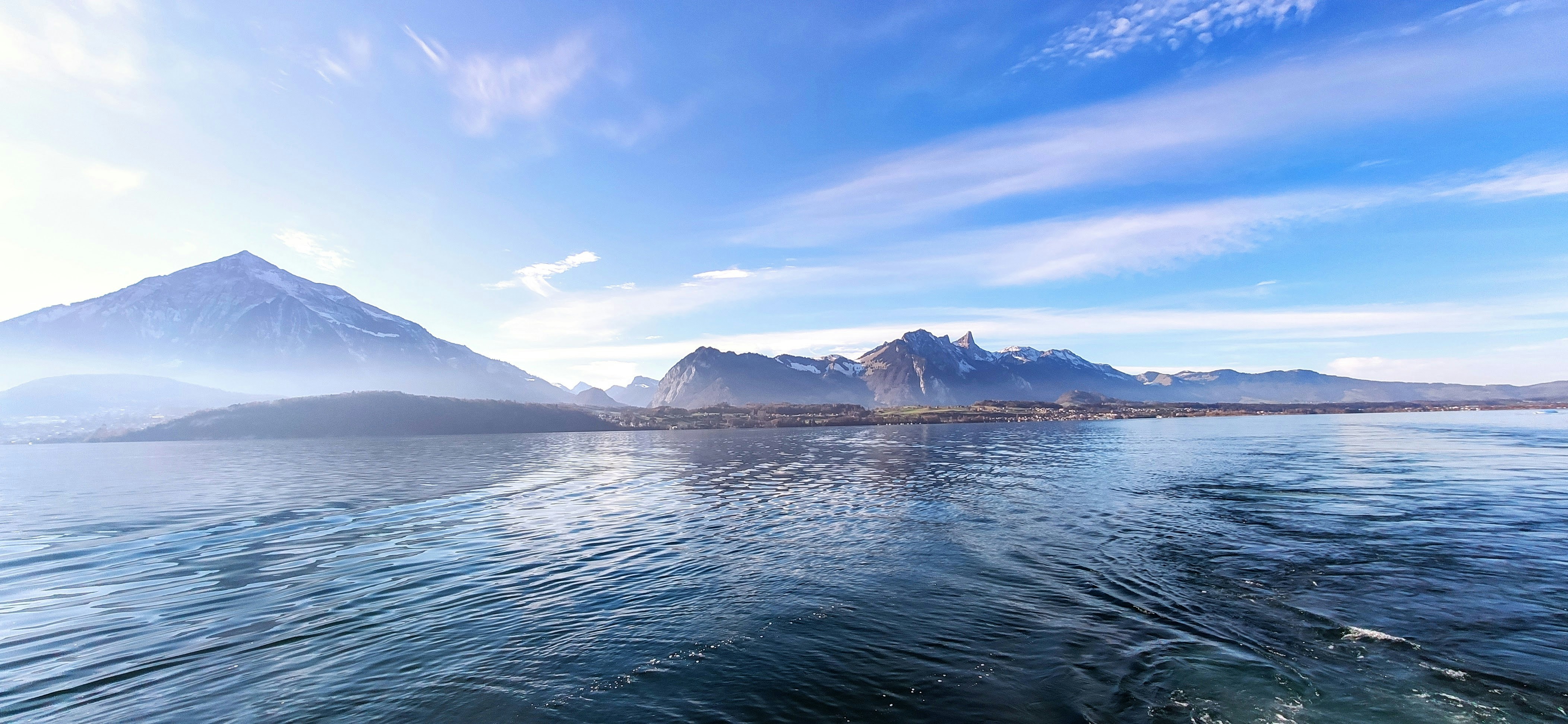 Snow-capped mountains reflected in the still waters of Lake Thun under a blue sky.
