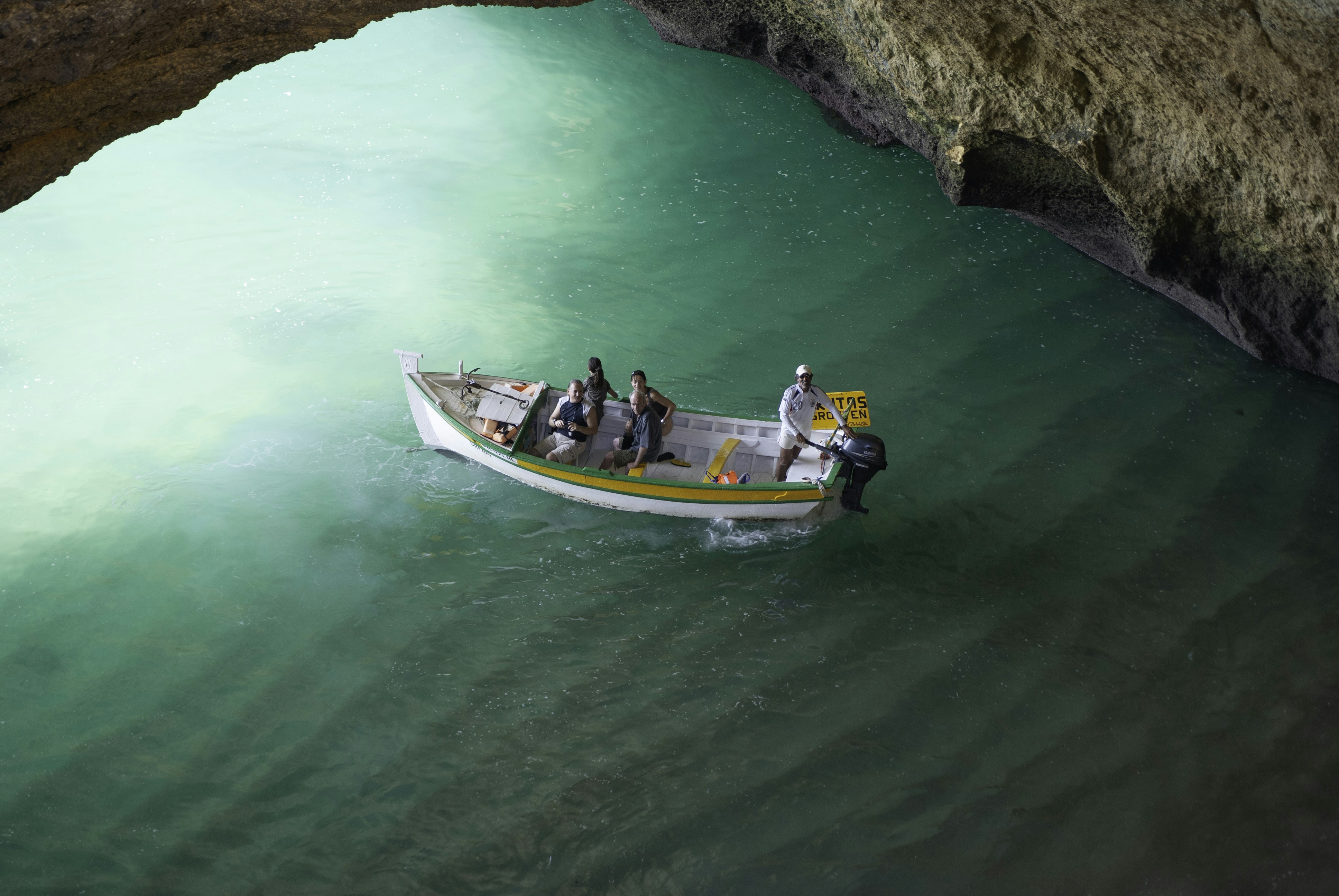 A small boat navigates through turquoise waters under a natural rock formation, showcasing the serene beauty of the cave environment.