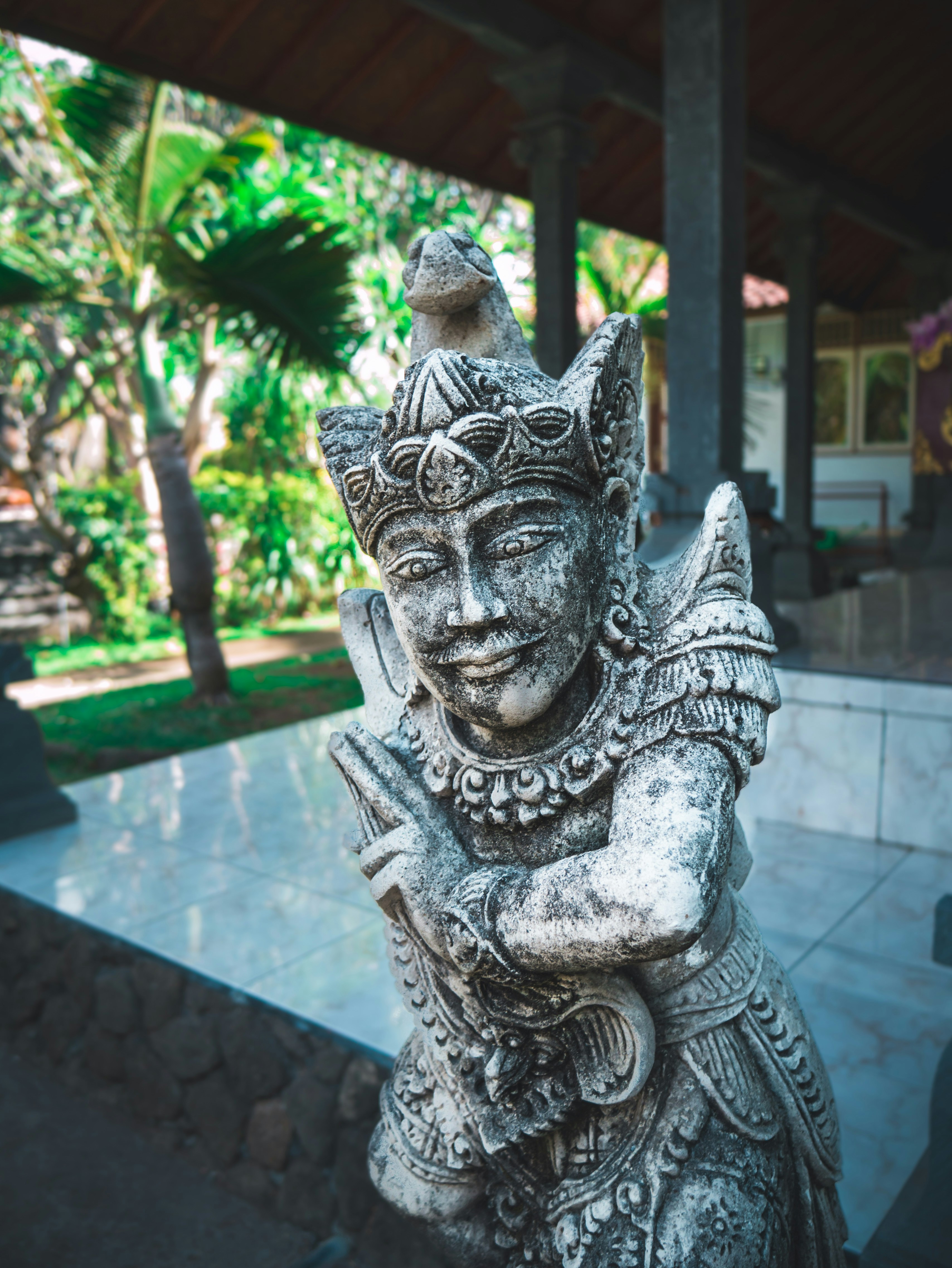 Granite Guardian by a Sunlit Terrace: Intricate Carvings & Tropical Backdrop