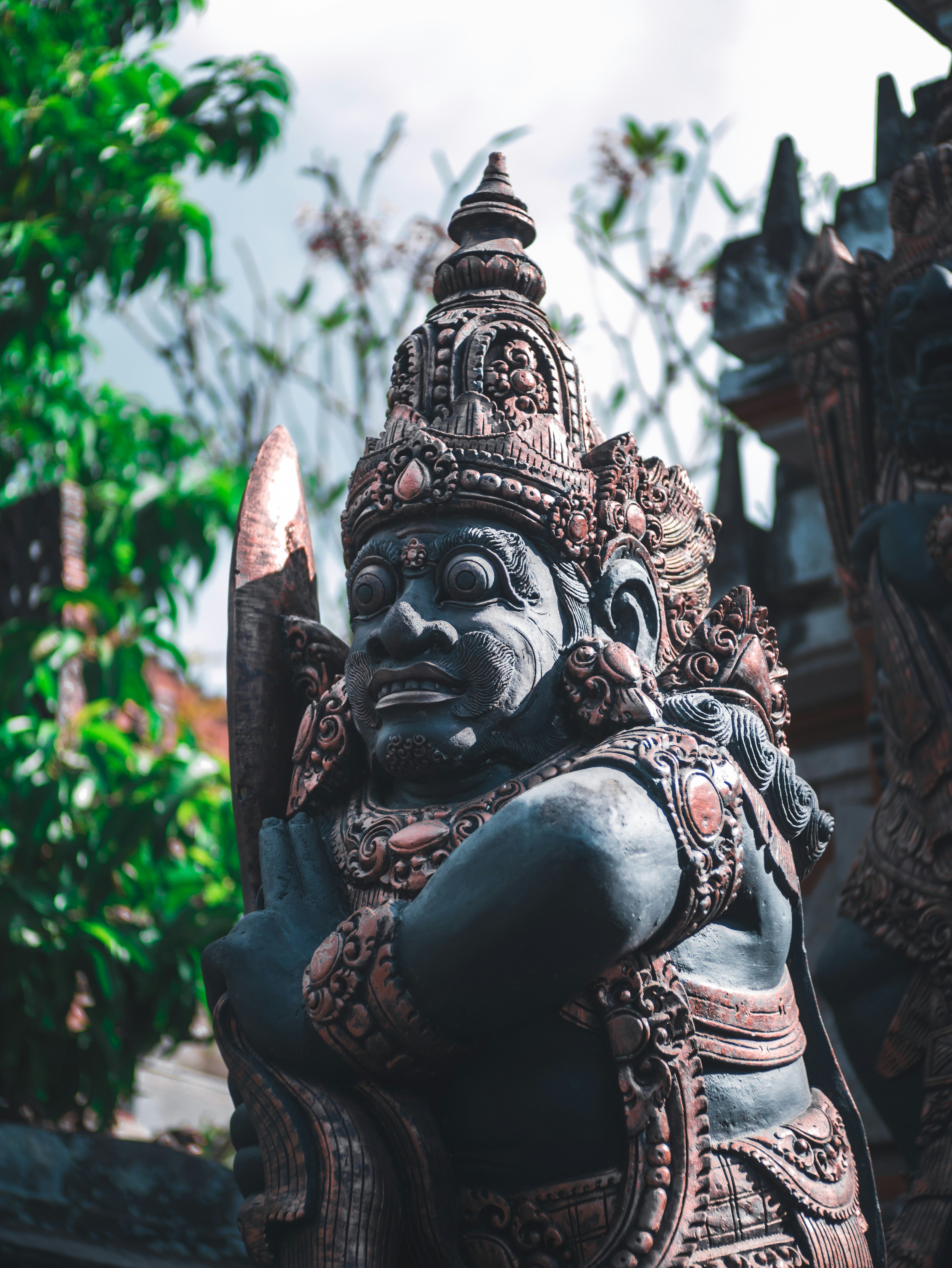 Intricately carved stone statue of a guardian deity at a Balinese temple, surrounded by lush greenery.