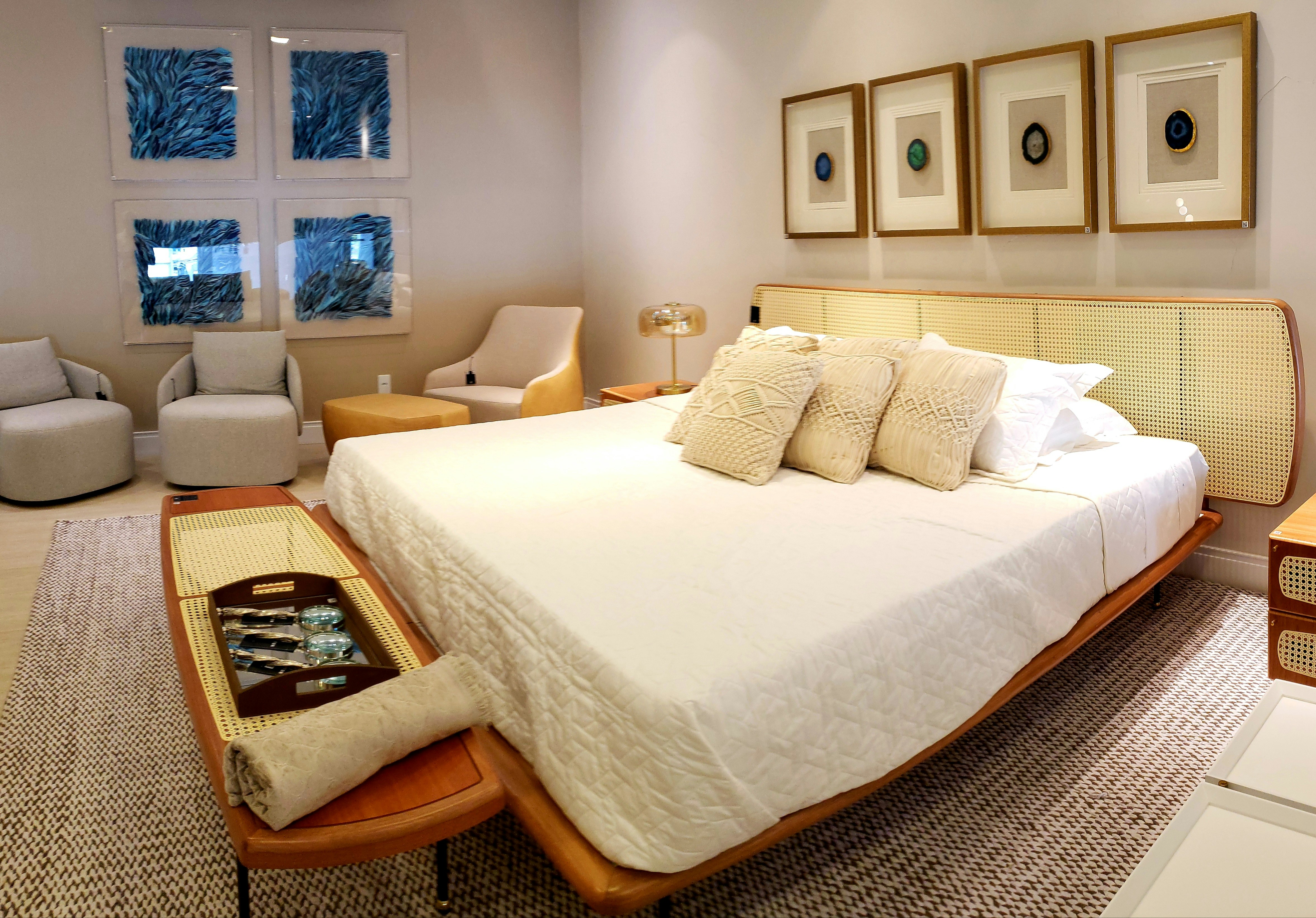 Elegant bedroom featuring a plush bed with decorative pillows, stylish armchairs, and framed art pieces on the wall. A cozy atmosphere is enhanced by soft lighting.