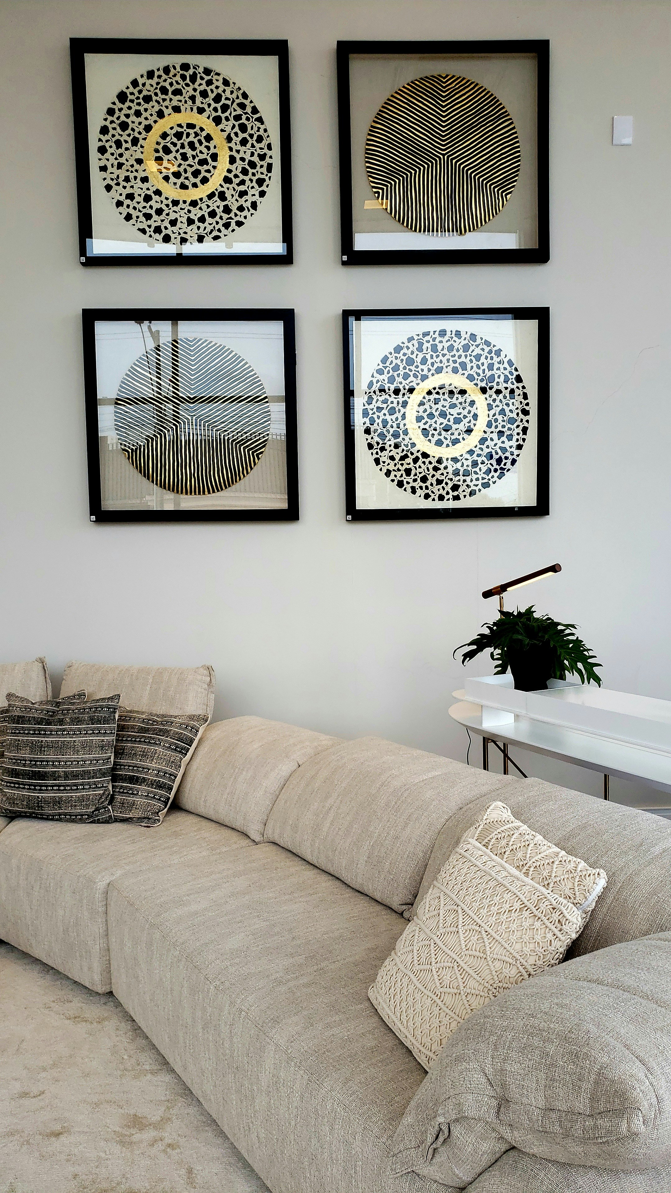 Four framed circular patterns with intricate designs above a beige sofa with textured pillows.