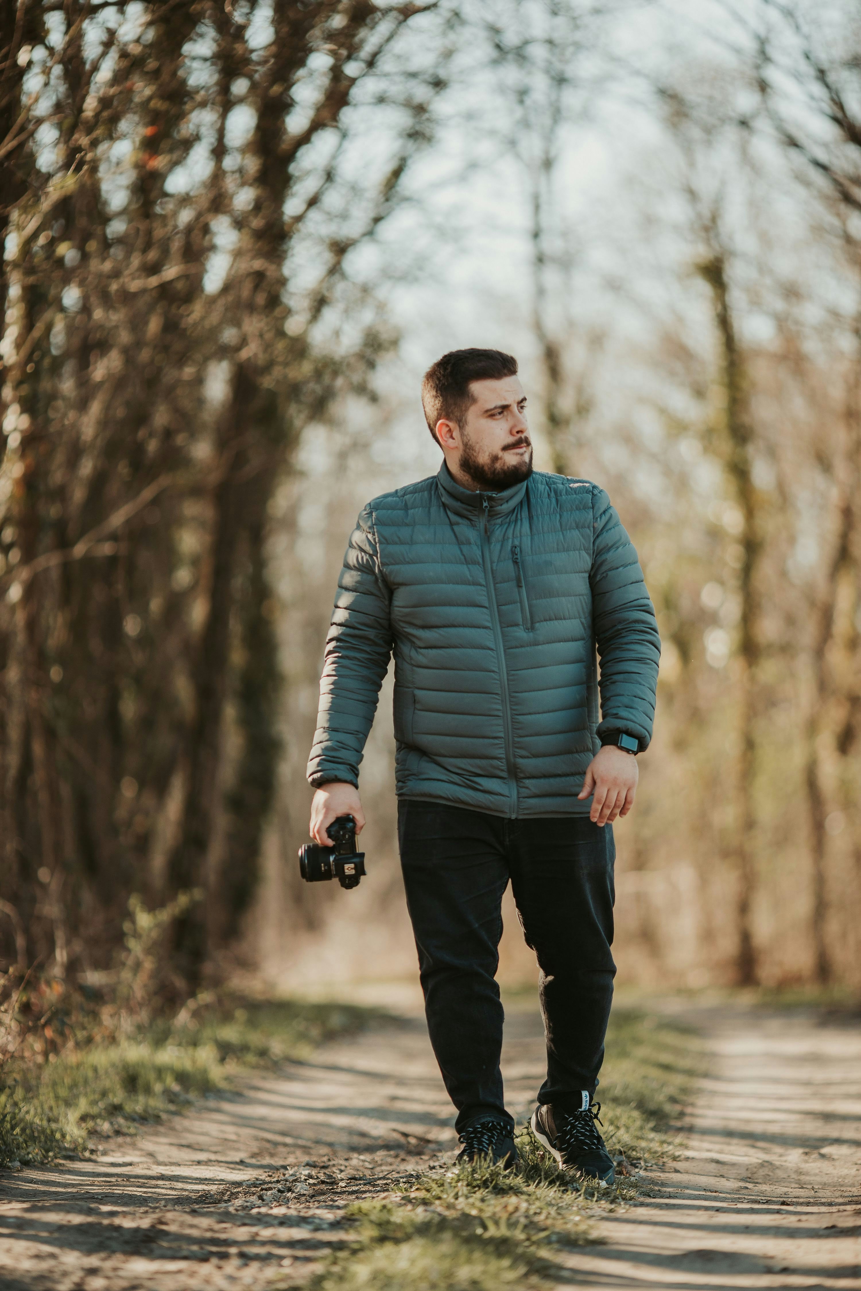 A lone photographer strides through a sunlit path, jacketed for the chill