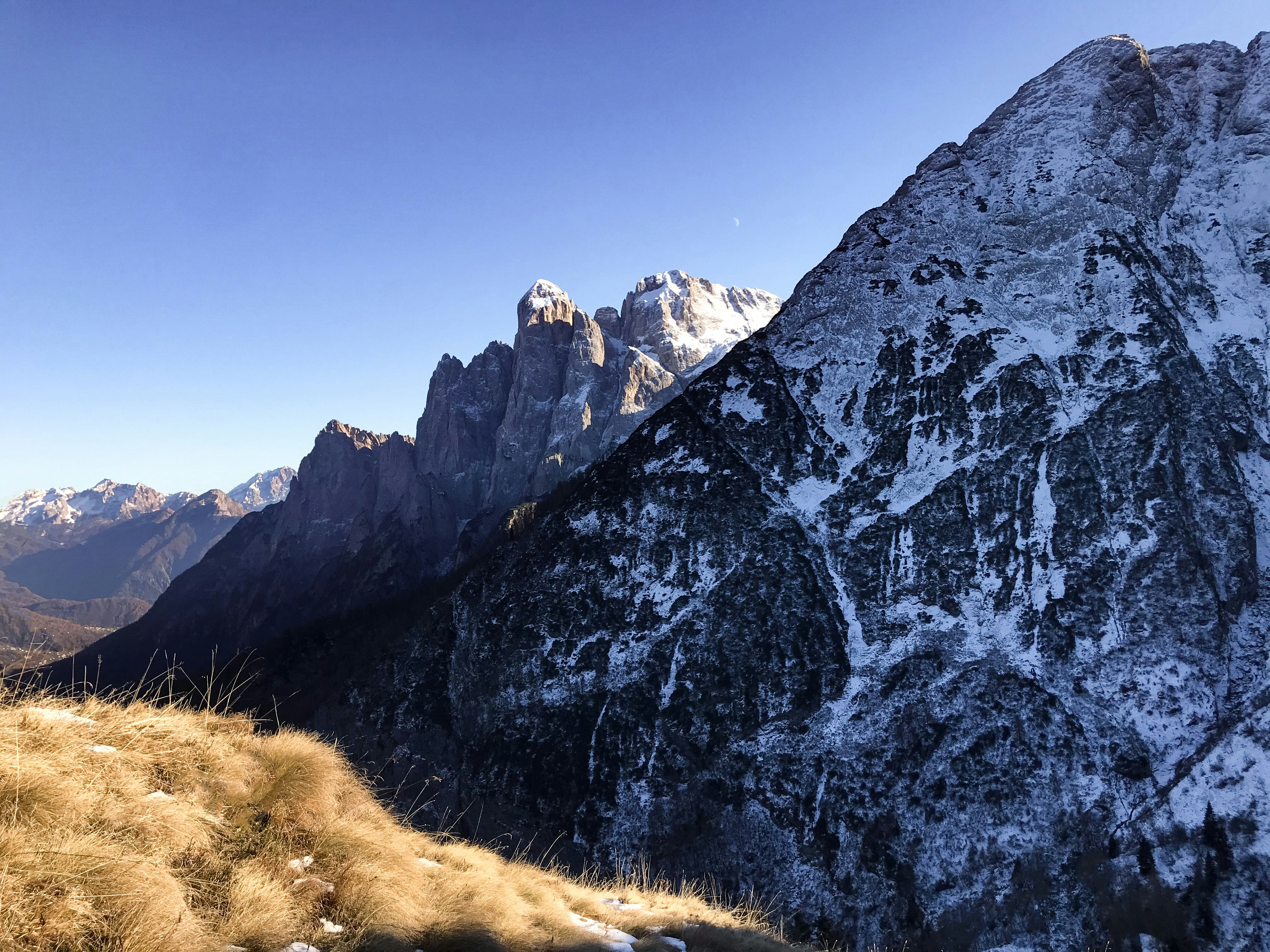 Snow-capped peaks rise majestically against a clear blue sky, with grassy slopes framing the scene. The rugged terrain showcases the raw beauty of the mountains.