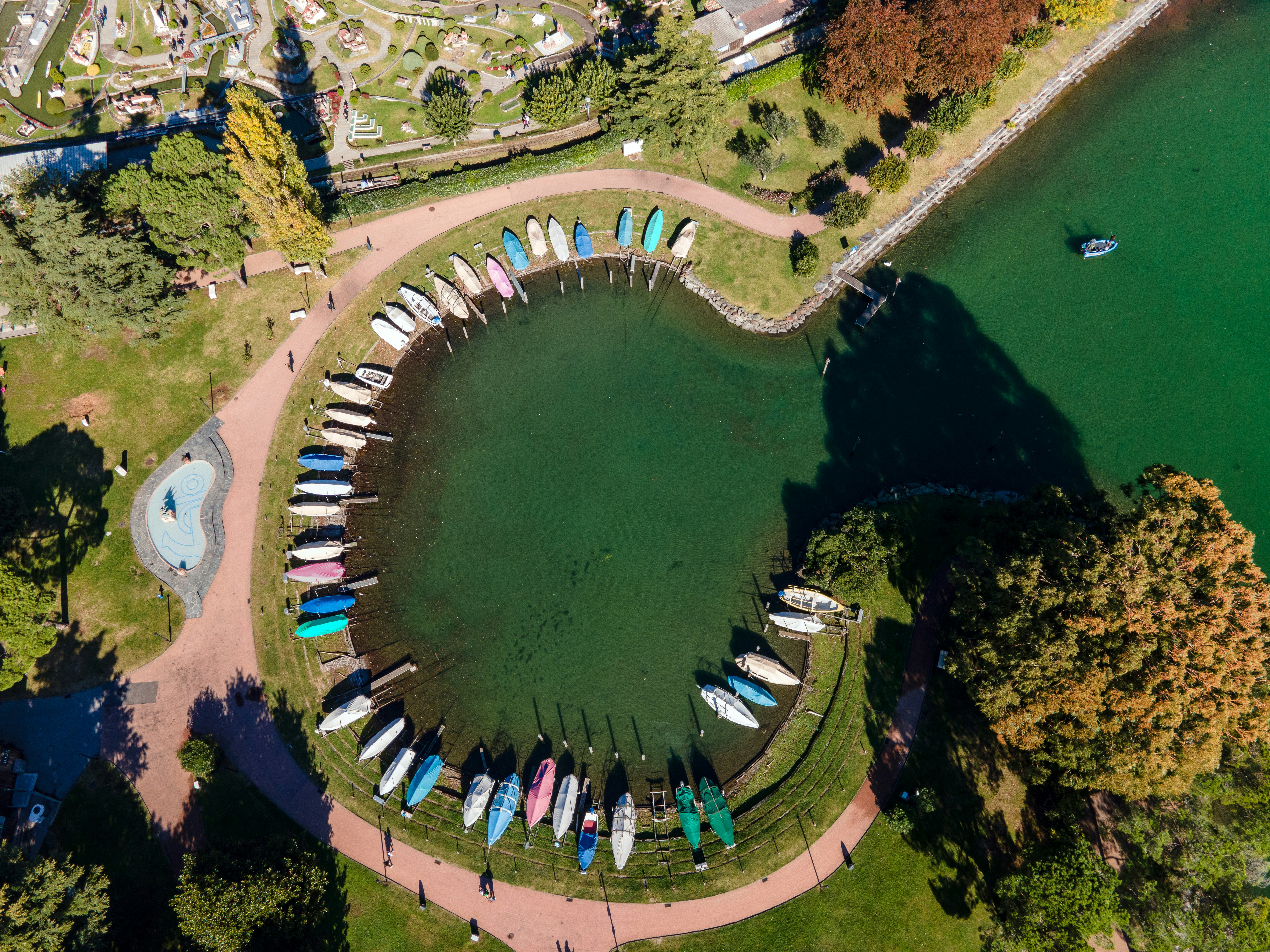 Aerial view of a circular dock filled with colorful boats, surrounded by lush greenery and pathways, showcasing a tranquil recreational area.